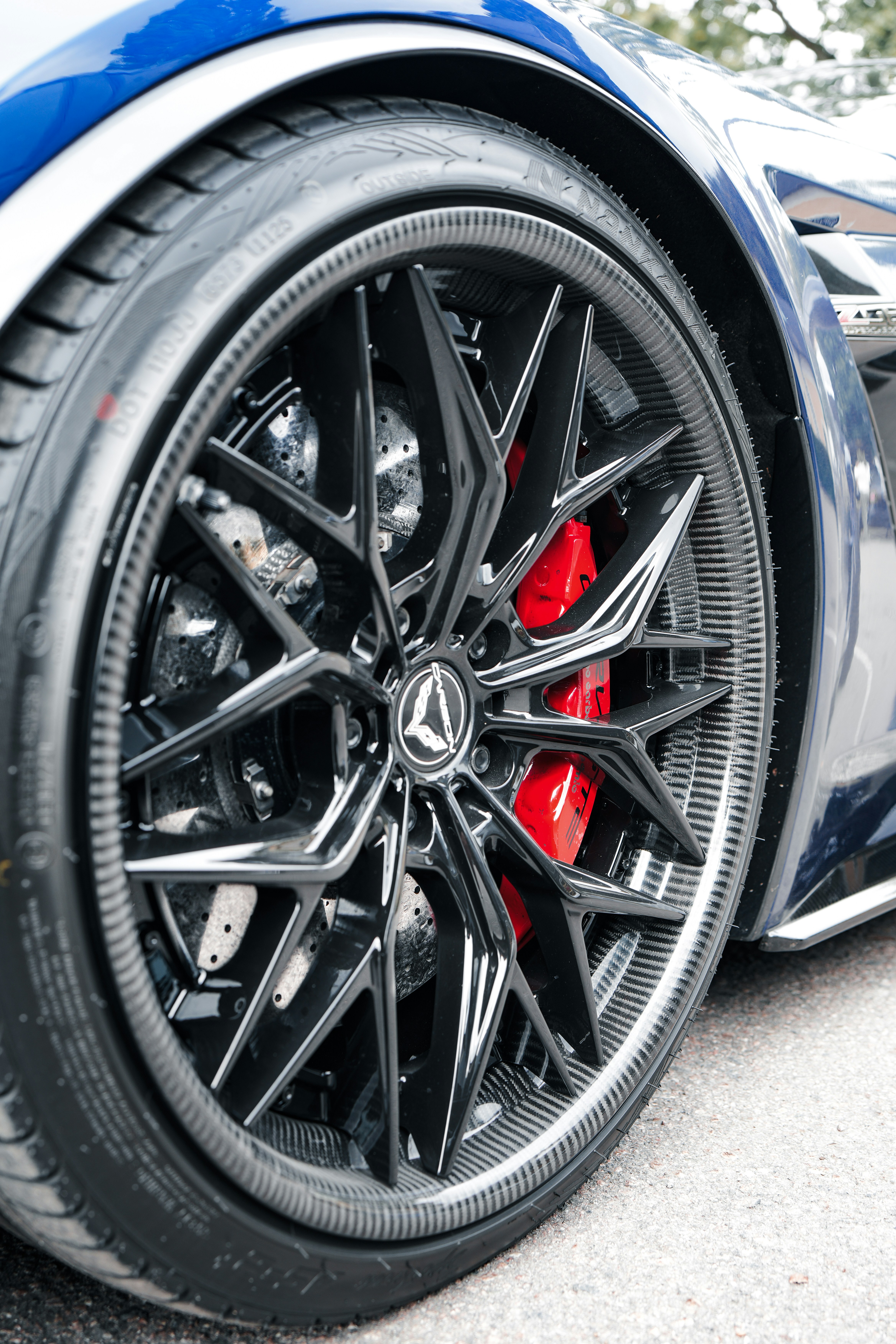 A close-up of a high-performance wheel: carbon spokes, red brake caliper, and forged details