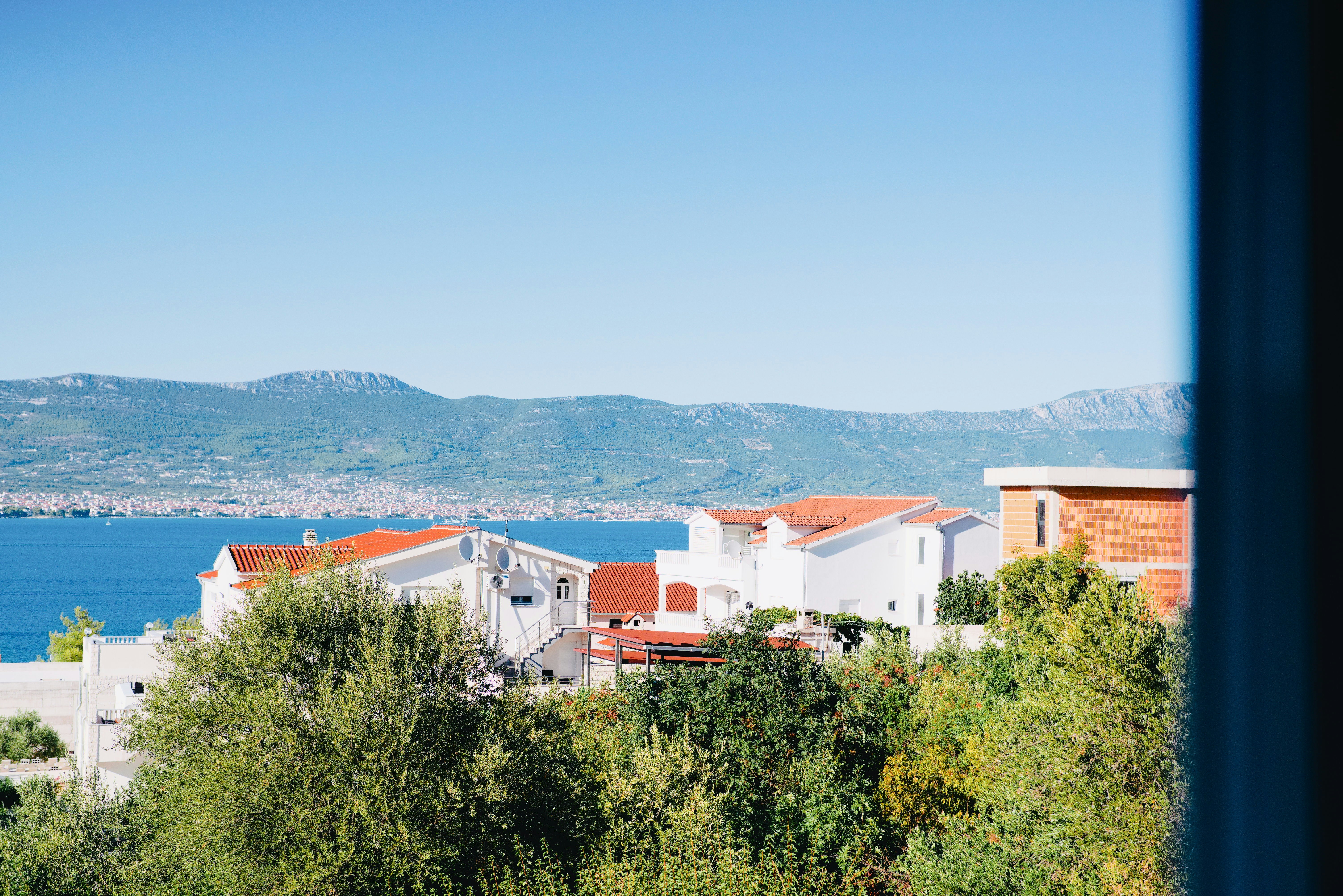 Sunlit seaside village framed by greenery and distant hills