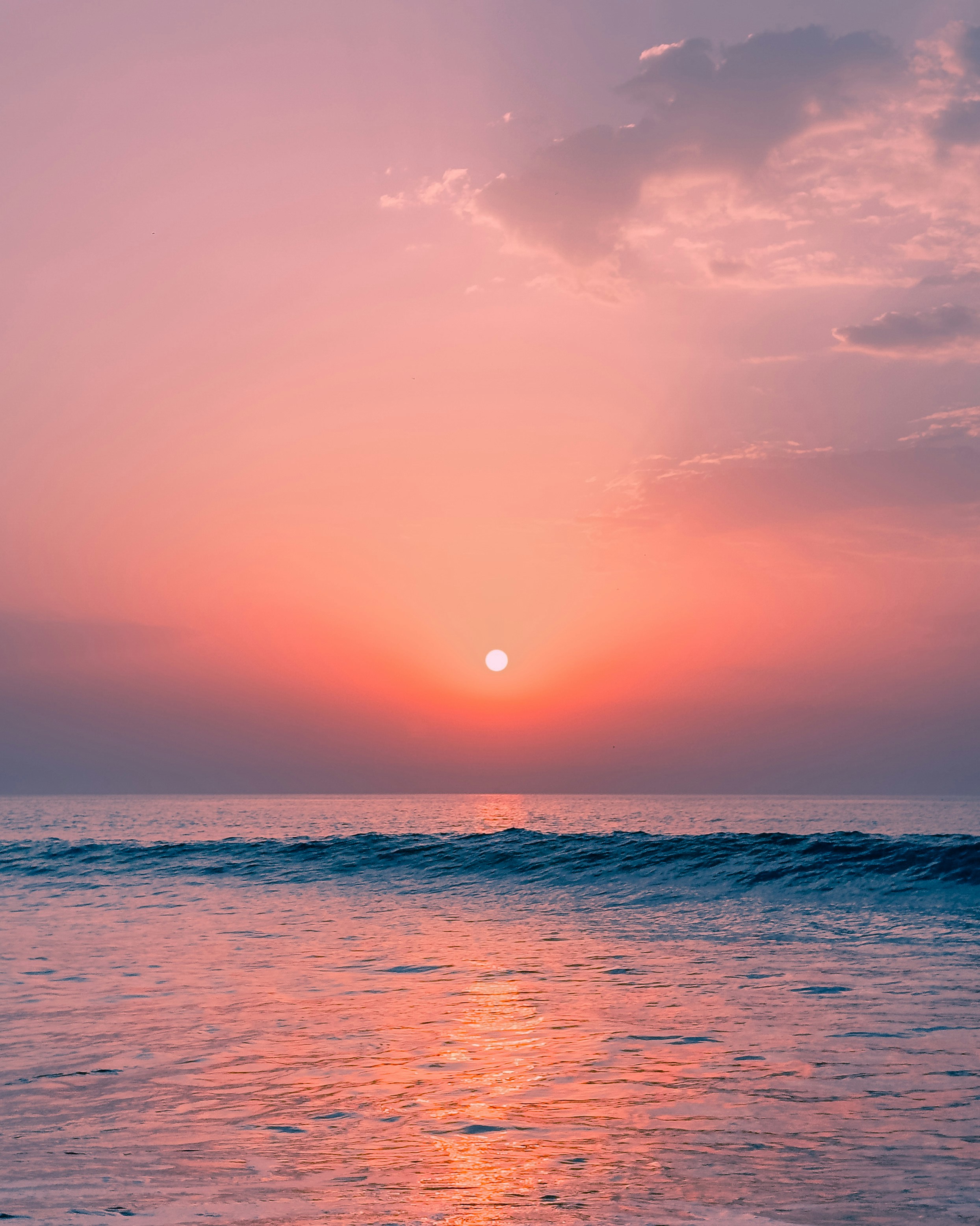 Sunset over a calm ocean with a warm pink-orange sky and soft waves; the horizon line marks the calm gradient of color across the water.