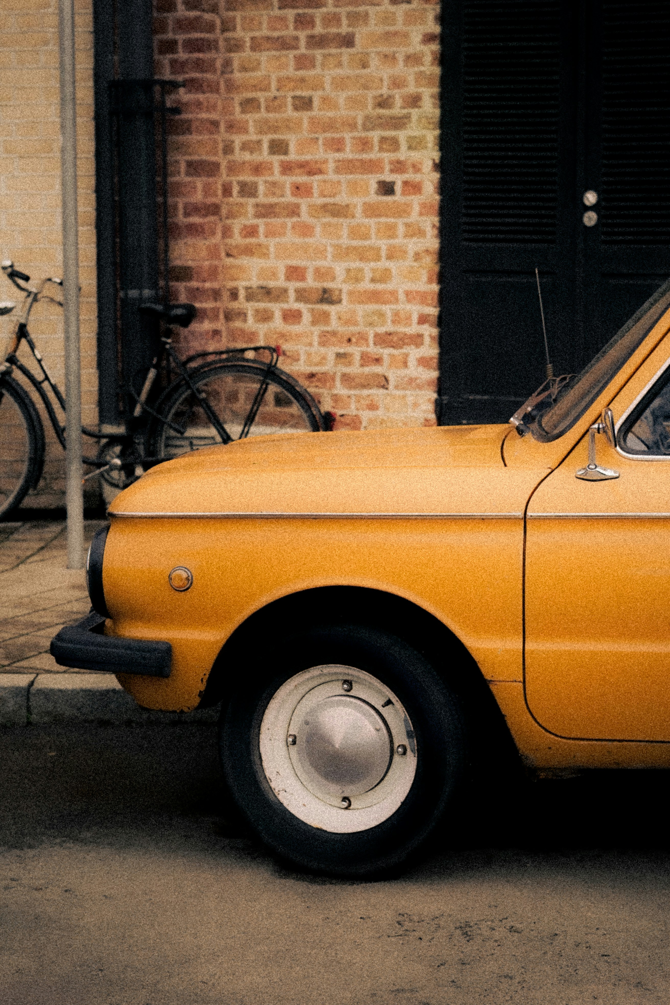 Amber Idle: The Front Quarter of a Retro Yellow Car Resting by a Brick Wall