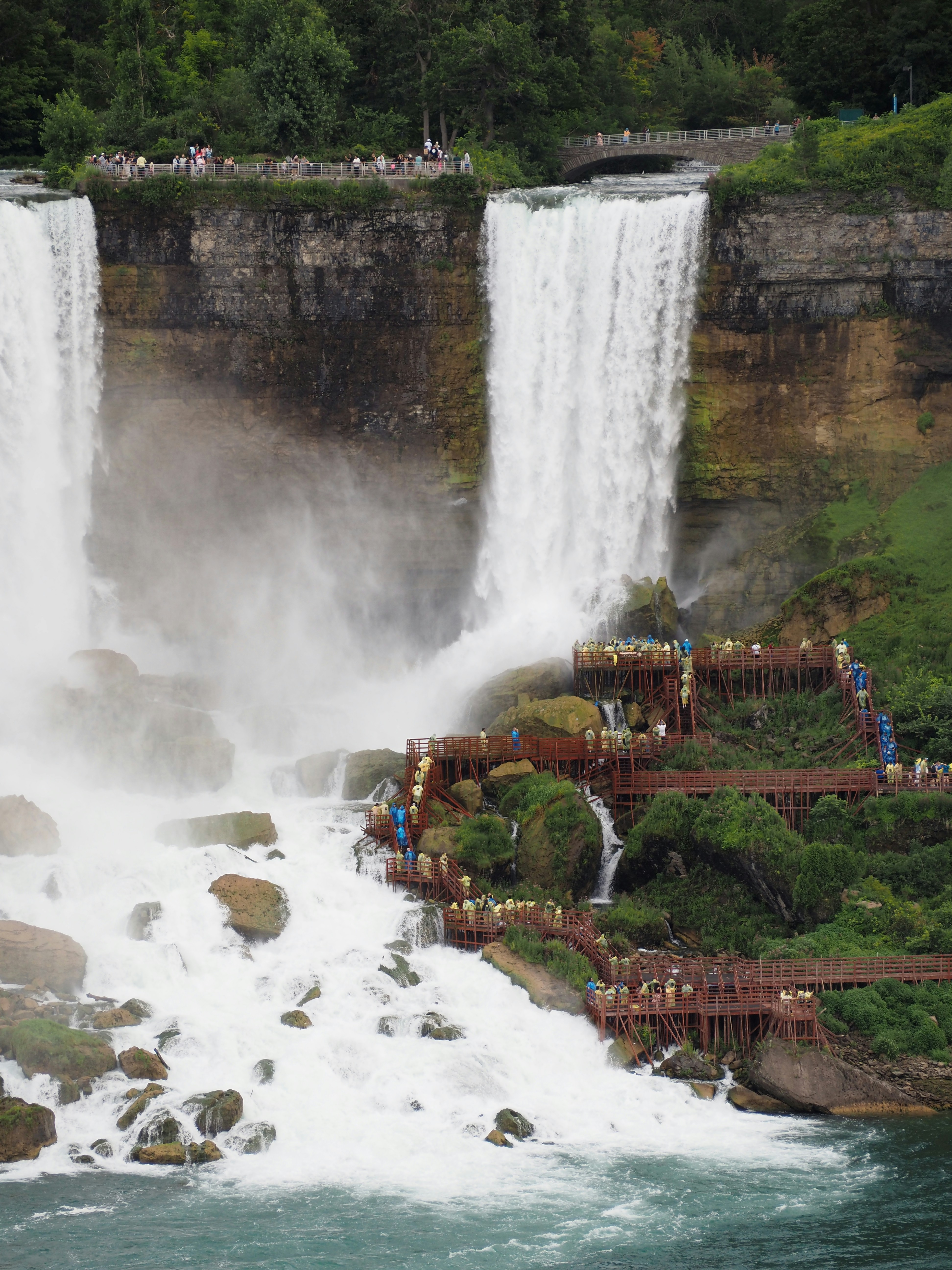 Mist-laced cascades crash over a cliff as visitors traverse wooden observation platforms along the gorge.