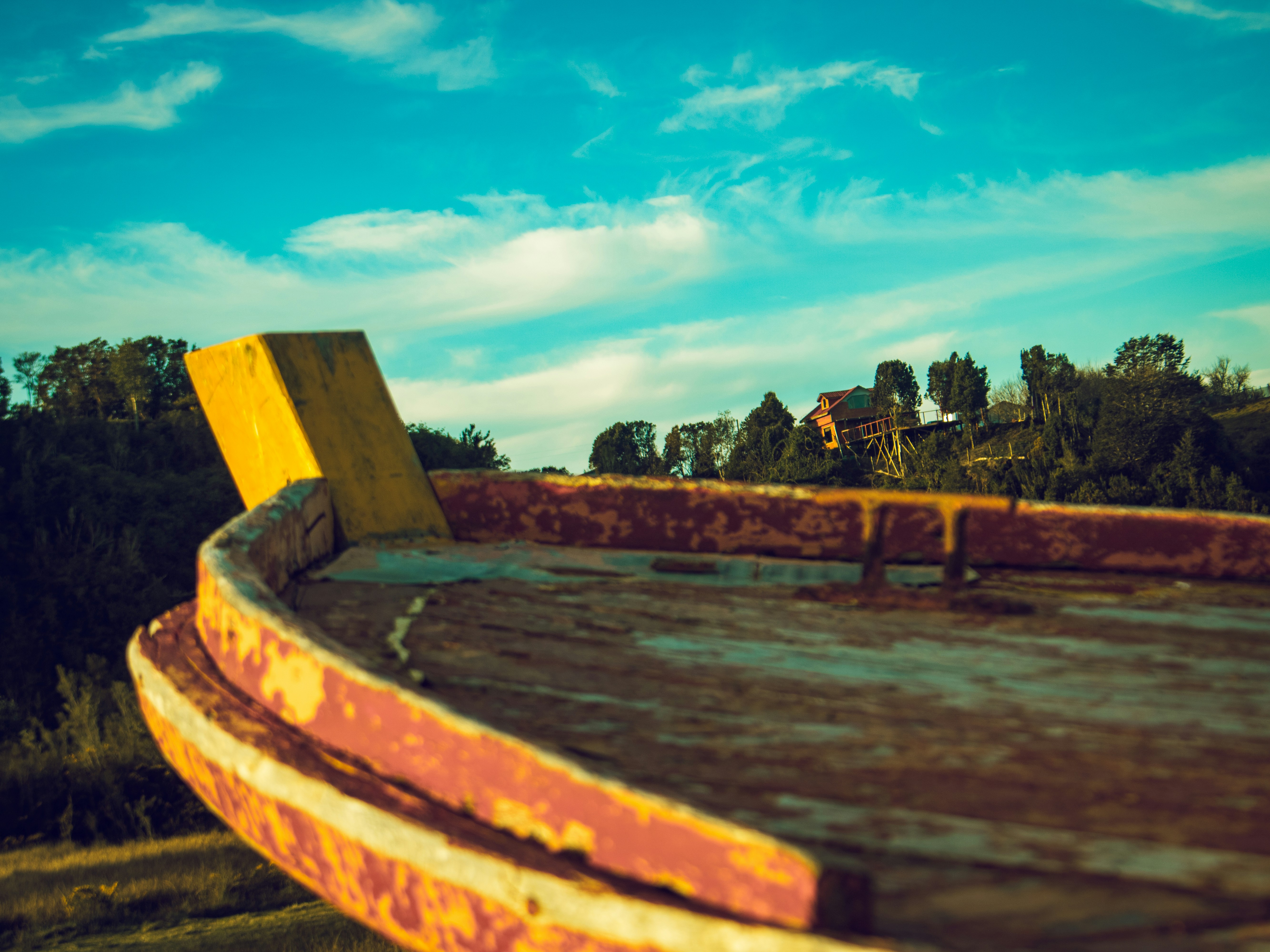 Weathered boat deck sits in foreground with chipped red paint, hills and trees in distance under a bright blue sky.