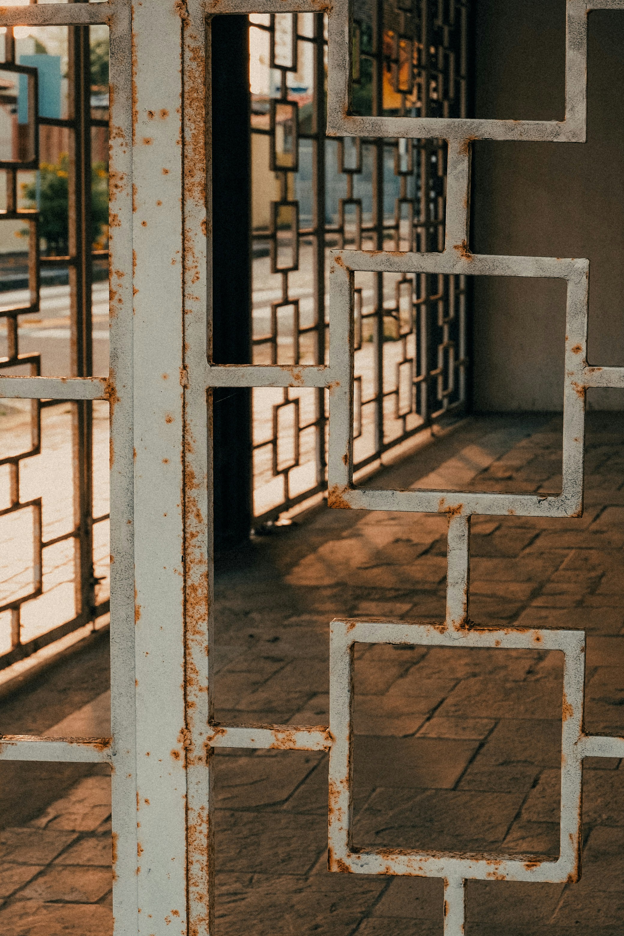 A weathered white metal gate with geometric square patterns and patches of rust