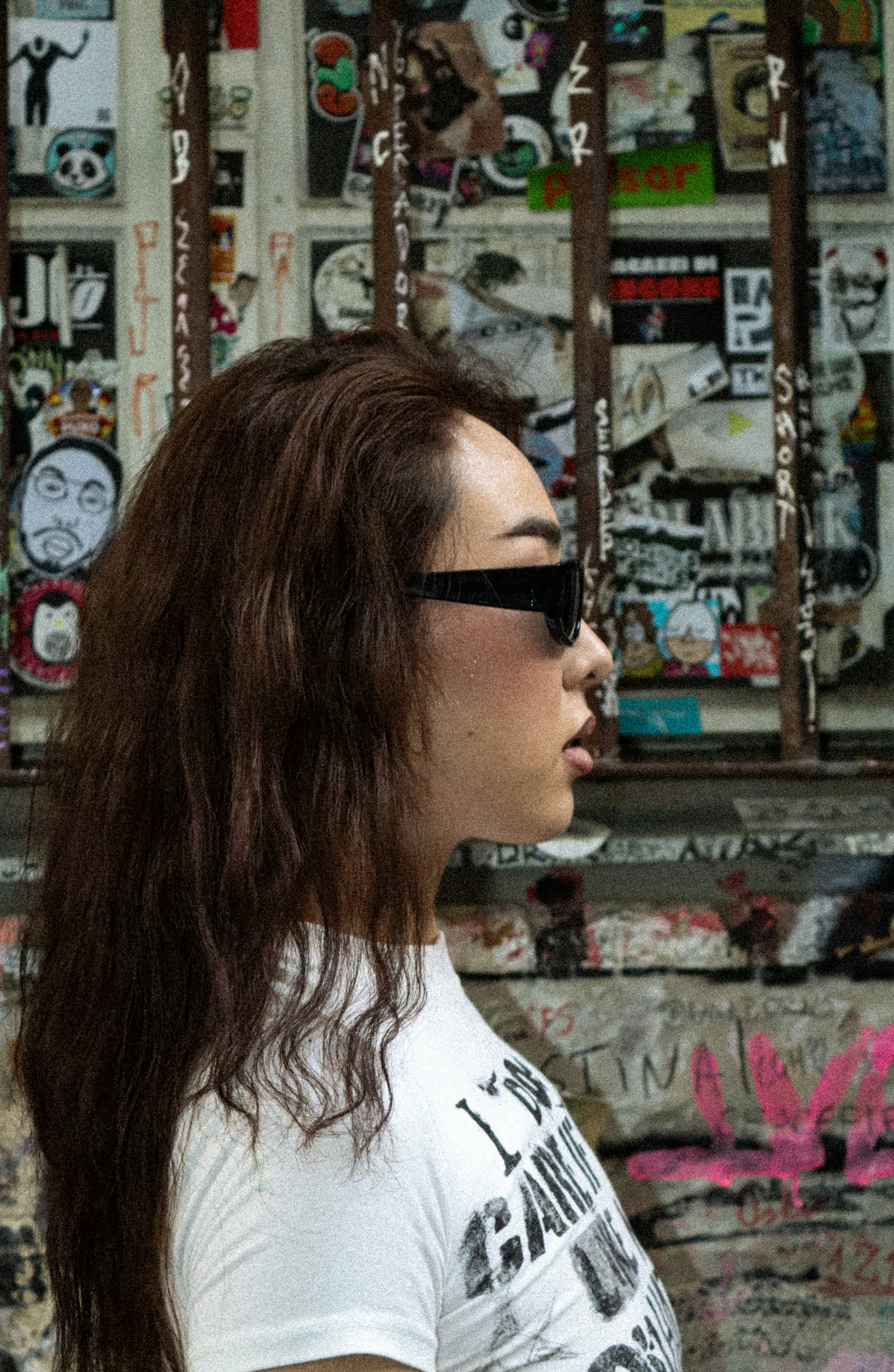 Profile of a woman wearing sunglasses against a graffiti-covered wall, captured in a candid street scene.
