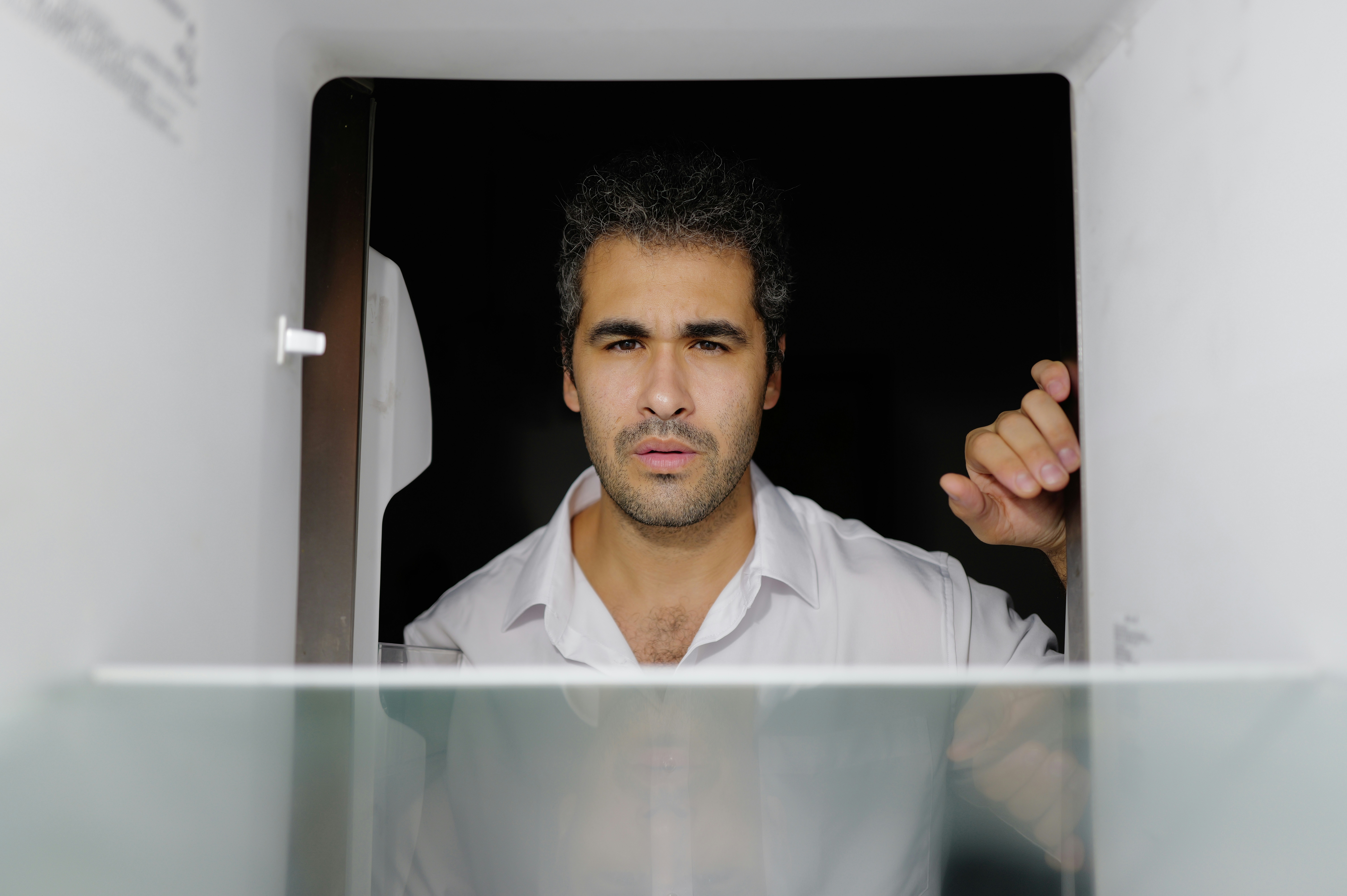Close-up portrait of a man centered in a small, hatch-like space with a dark background, suggesting a doorway or opening; the scene emphasizes expression and confinement.