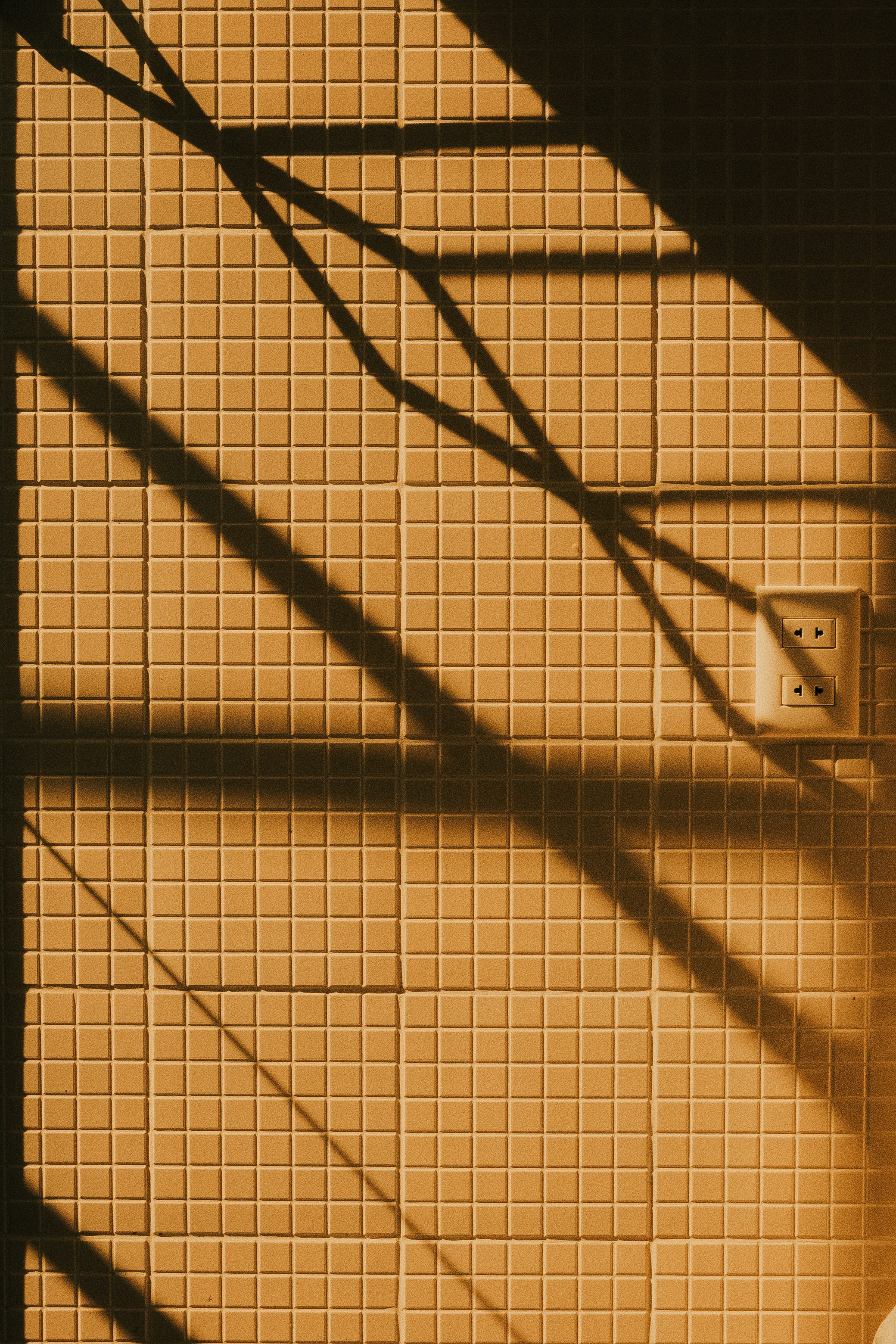 Shadowed Grid: Sunlit Tile Patterns Across a Coffee-Orange Wall