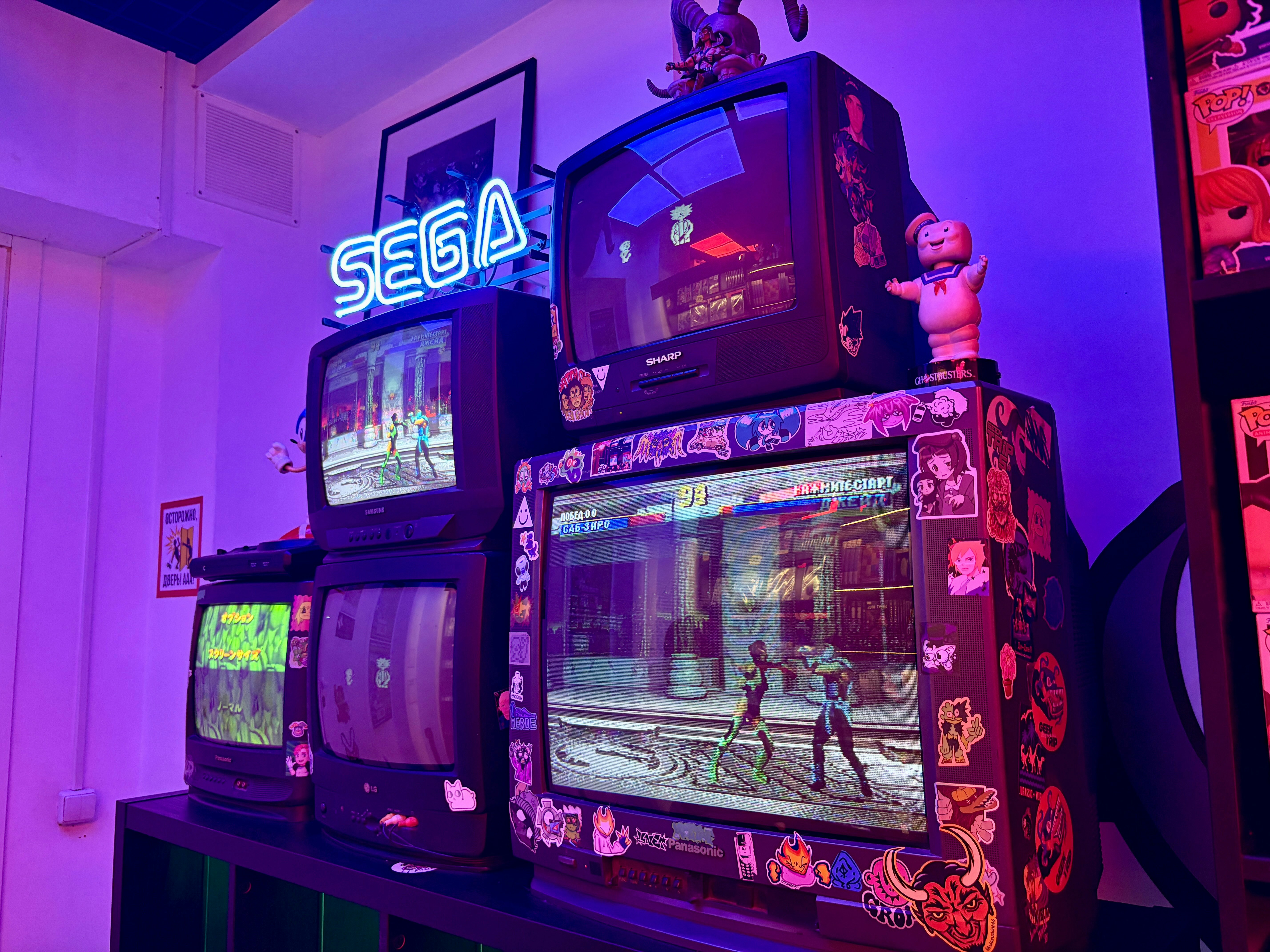 Multiple vintage televisions displaying fighting games under a neon SEGA sign in purple light