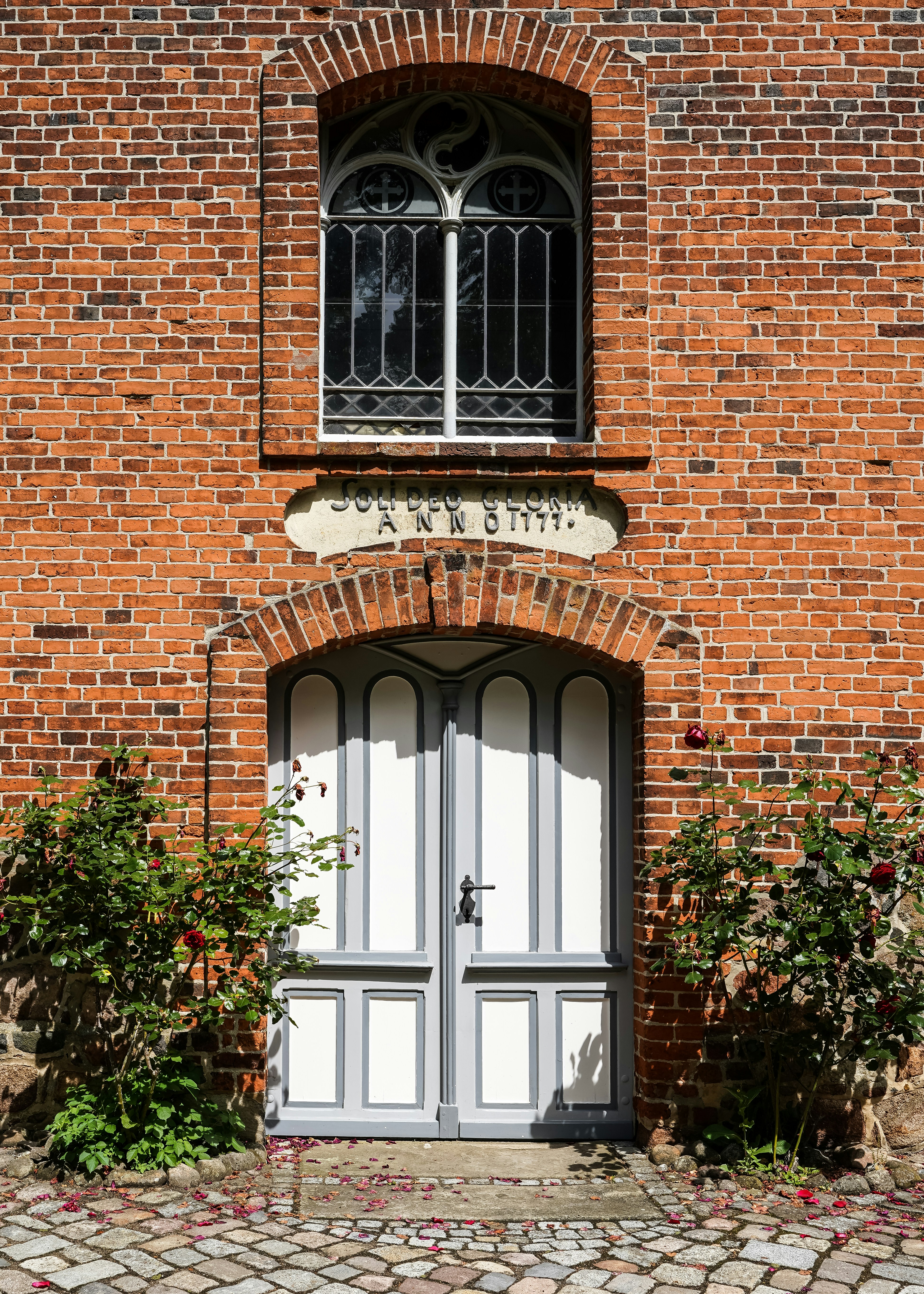 Brick Facade doorway framed by climbing roses under arched window