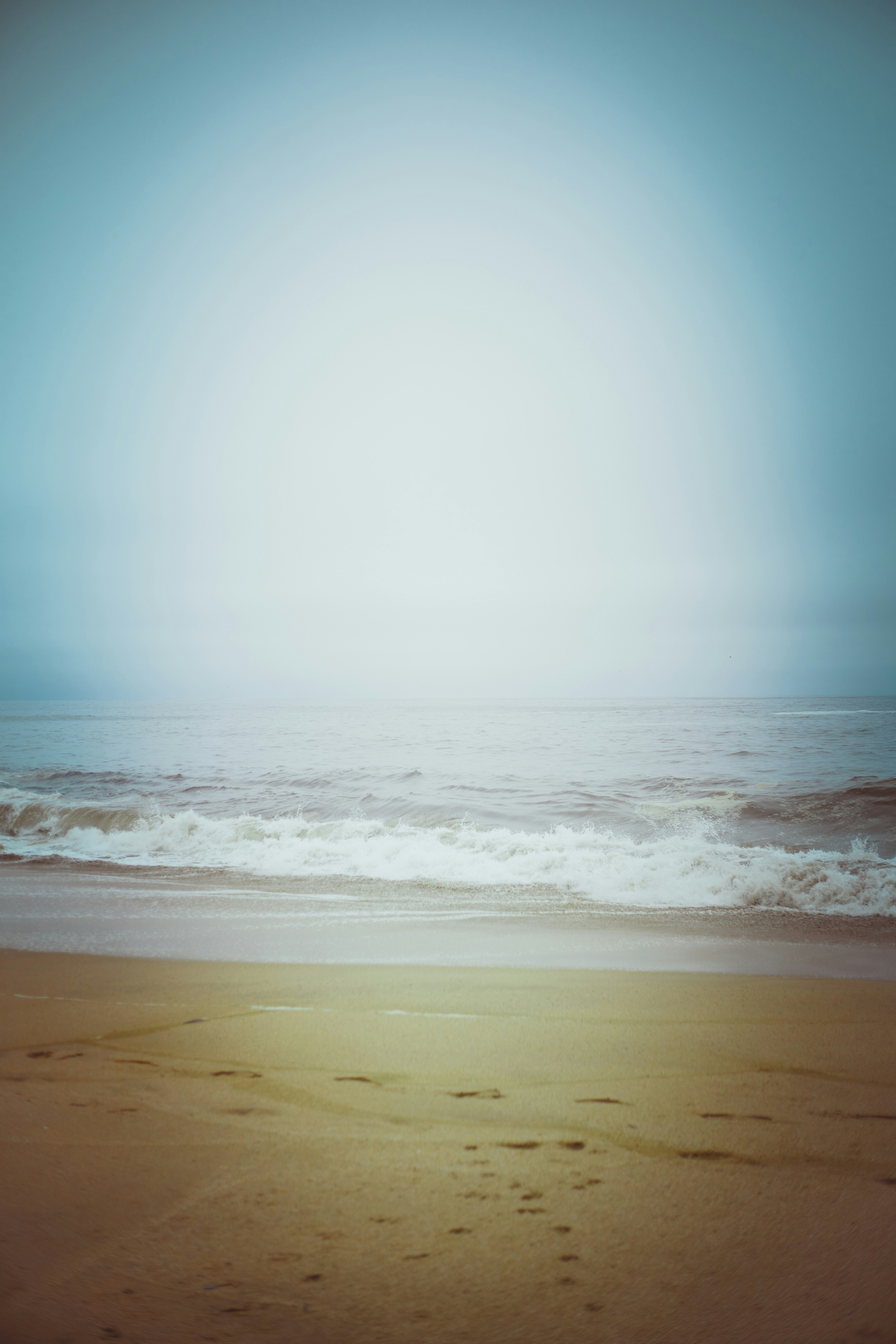 Soft-lit beach scene with a calm horizon and gentle waves; the image emphasizes airy sky and sandy foreground. A serene landscape without people, highlighting mood and color.