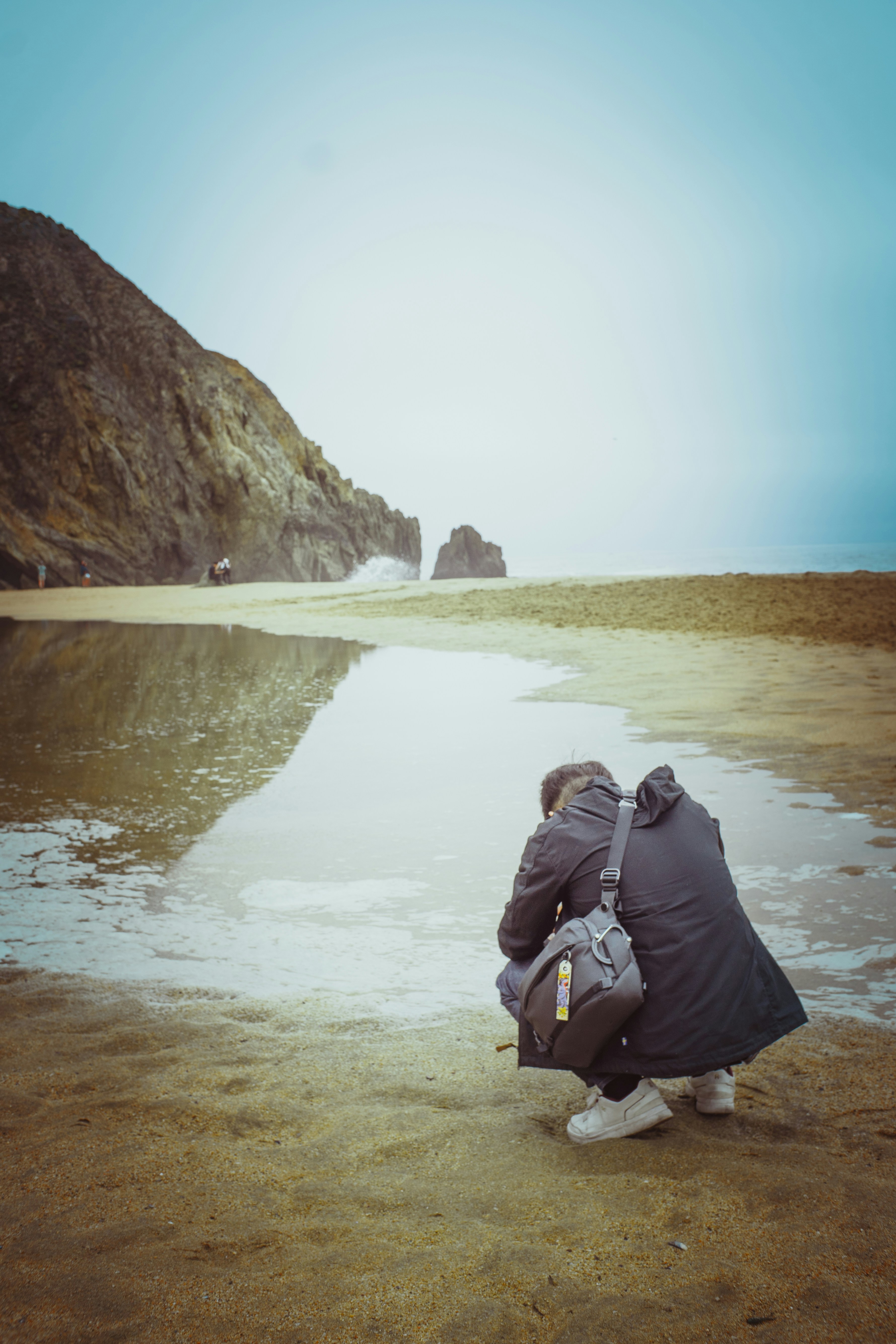 Kneeling on the Shore: A Quiet Moment with a Photographer by the Cliff