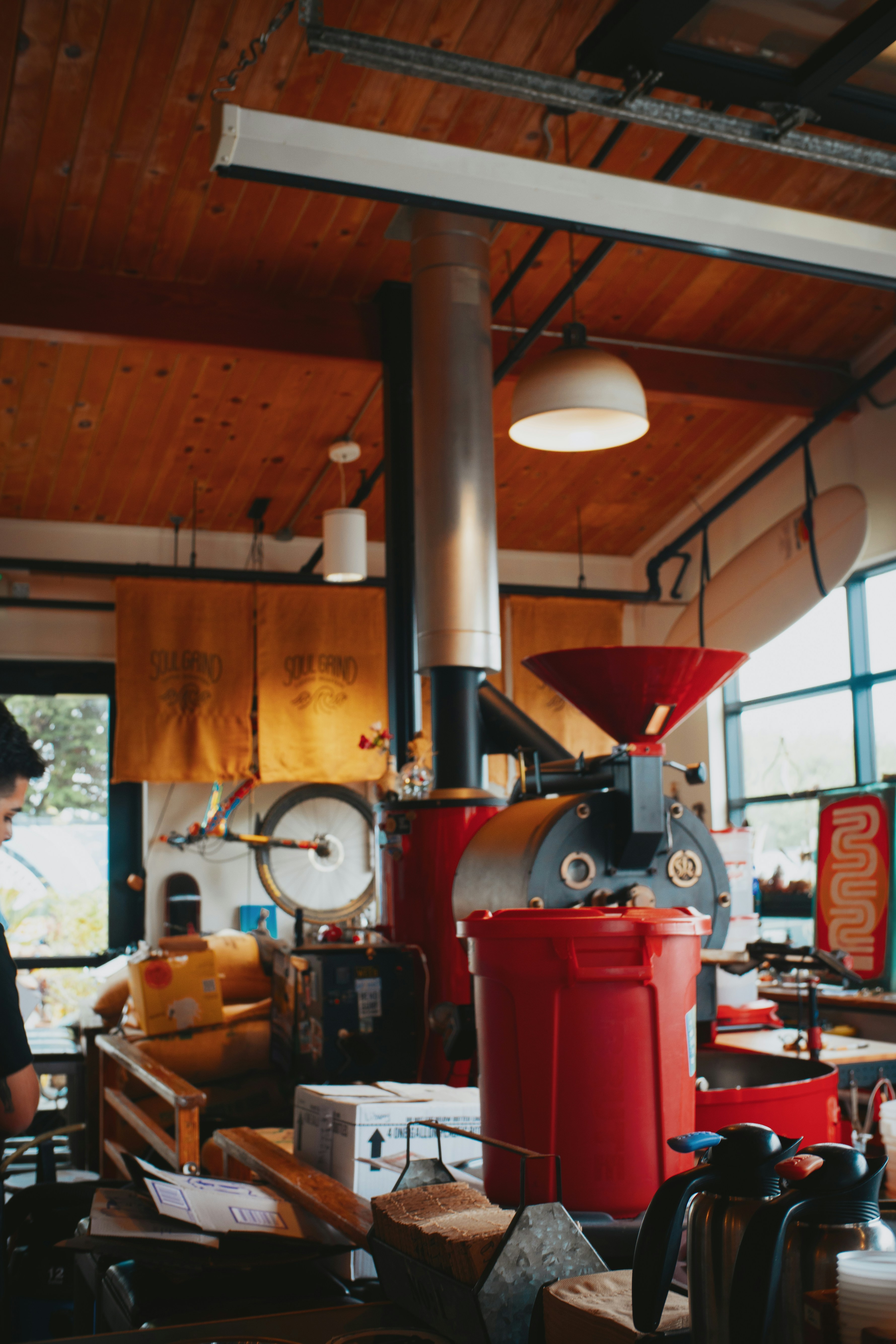 A red coffee roaster with a large hopper in a rustic workspace