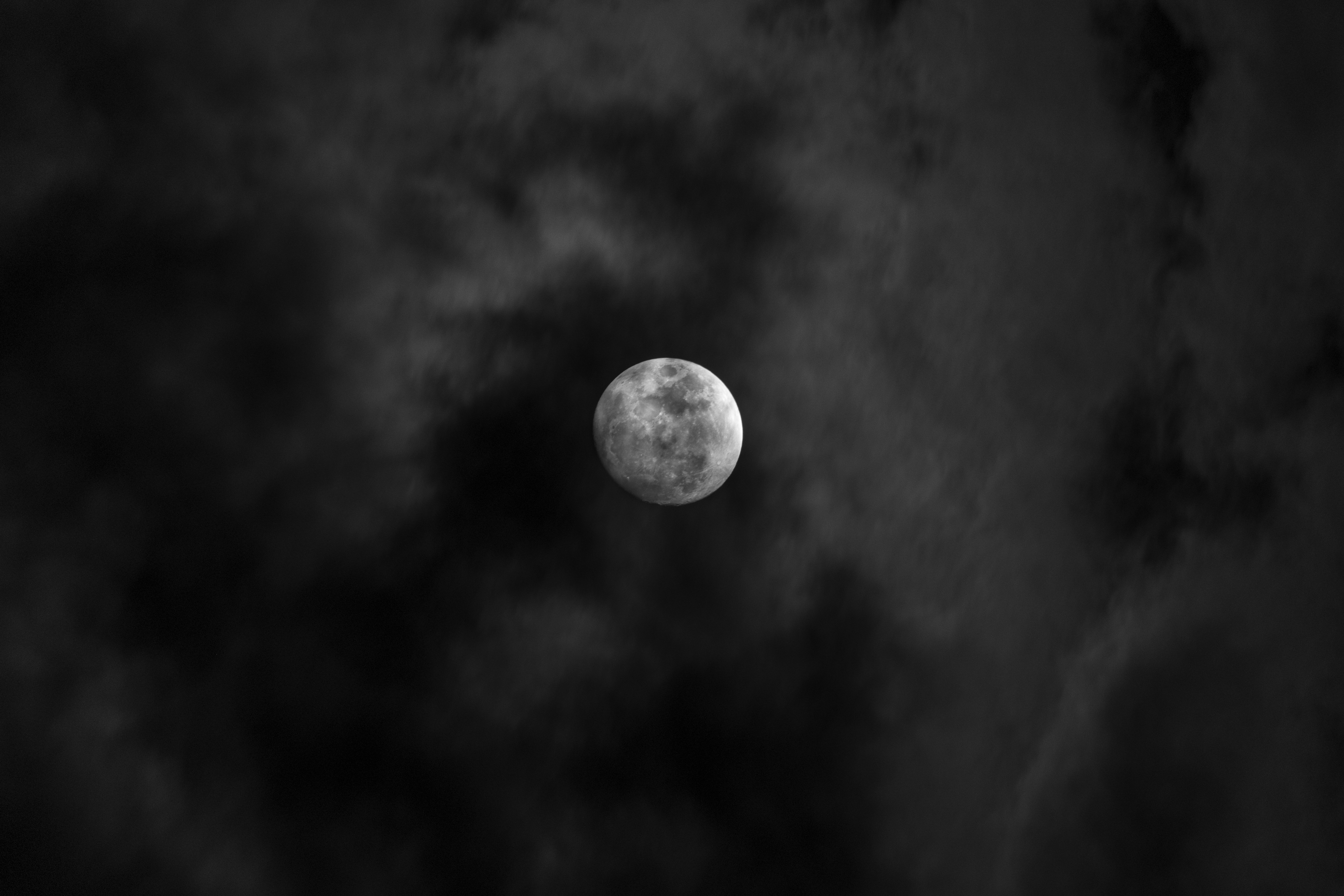 Moon glows softly through textured clouds in a monochrome nightscape.