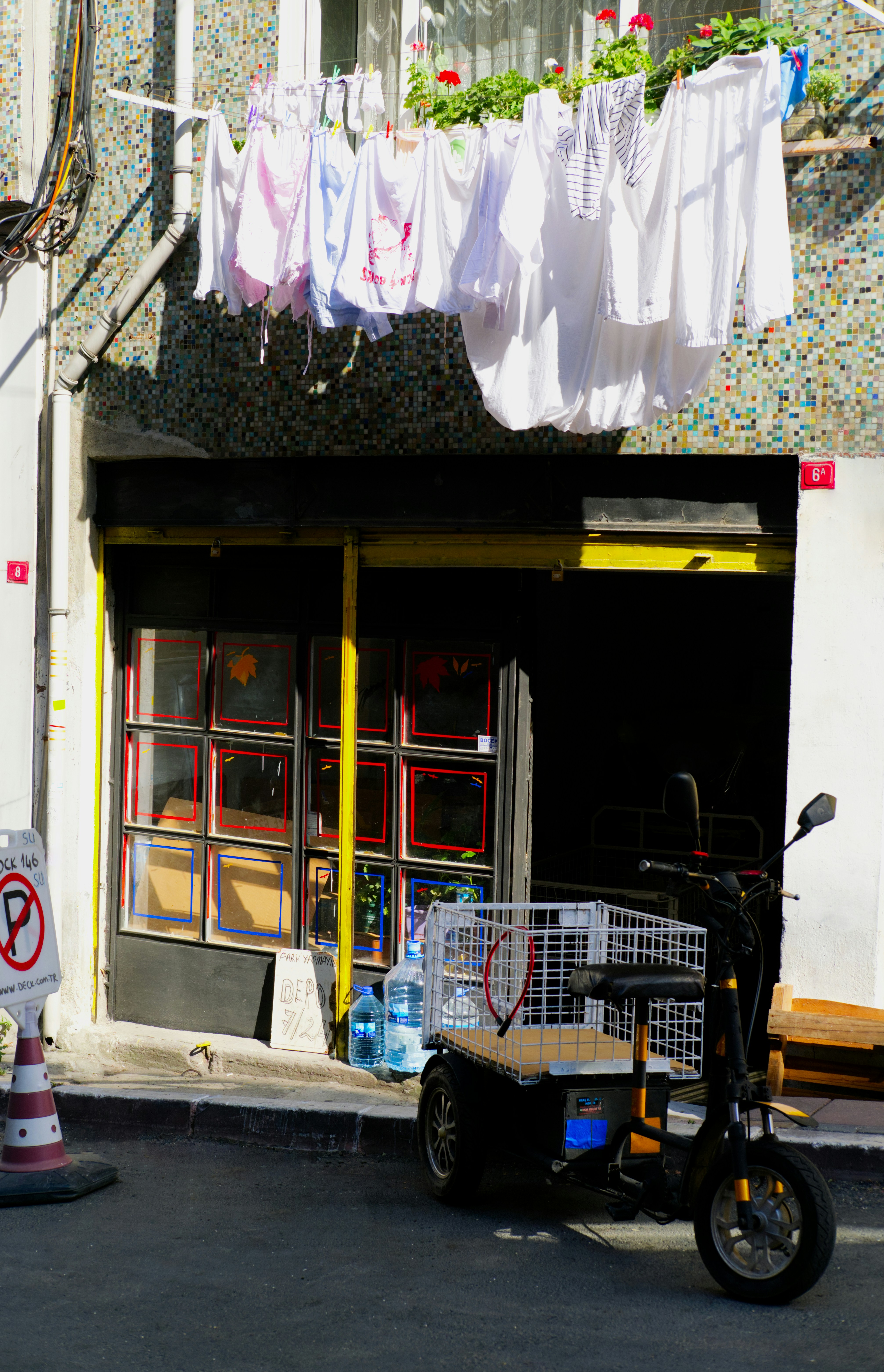 Laundry hanging on a line above a storefront with a parked electric tricycle