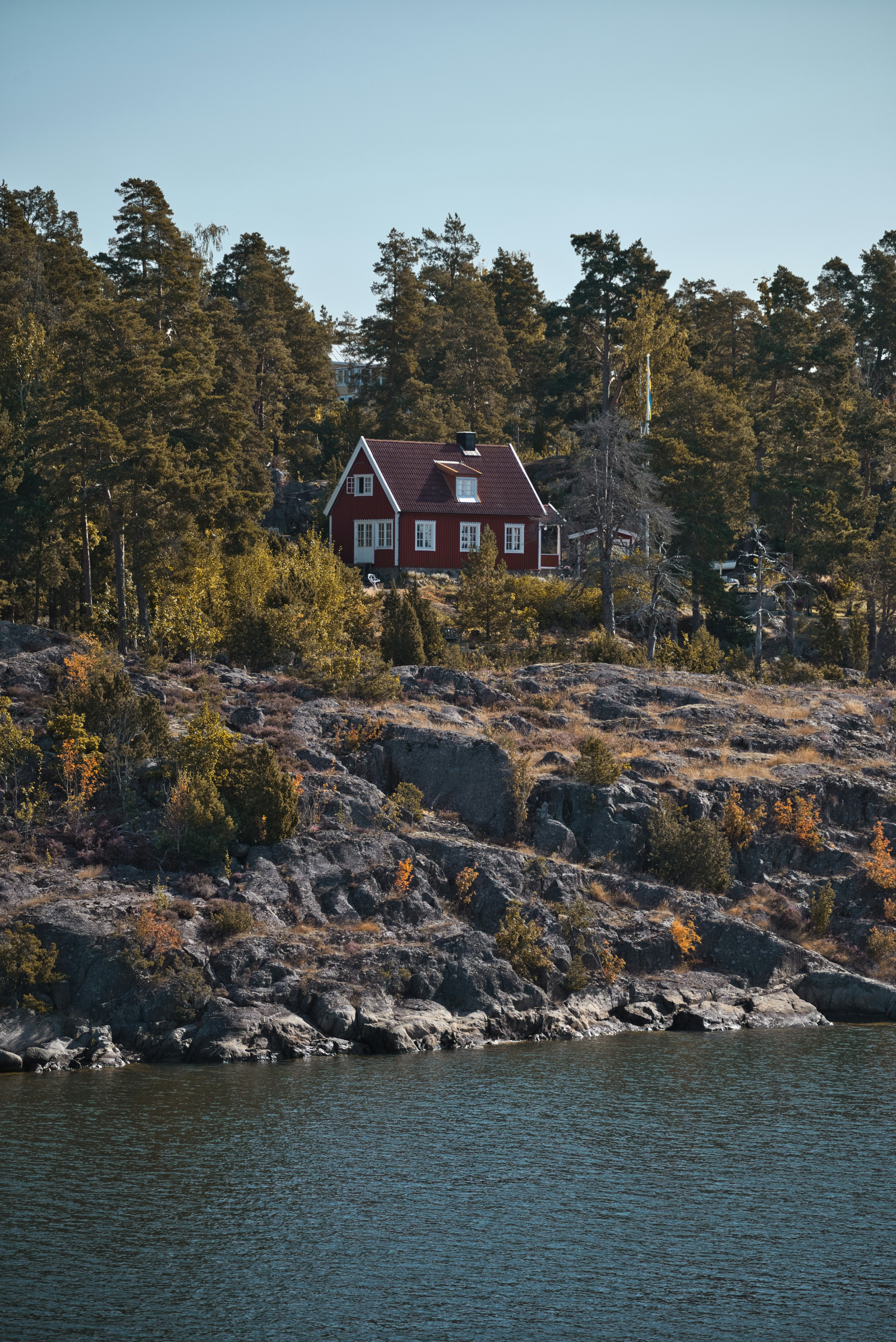 Red House on a rocky shoreline, framed by pines under a clear sky
