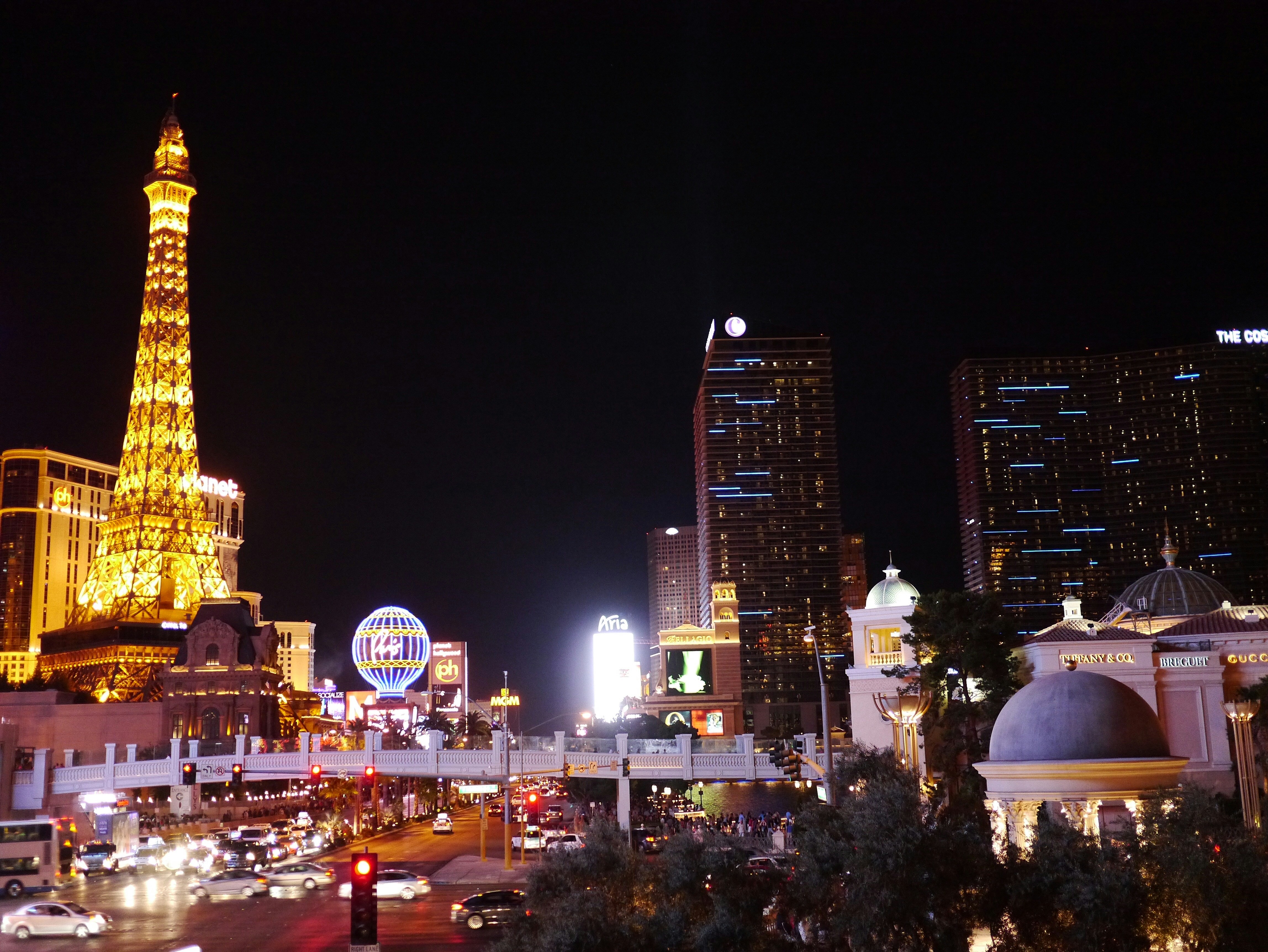 Nighttime cityscape with the Eiffel Tower replica and bright casino facades along a bustling Las Vegas street.