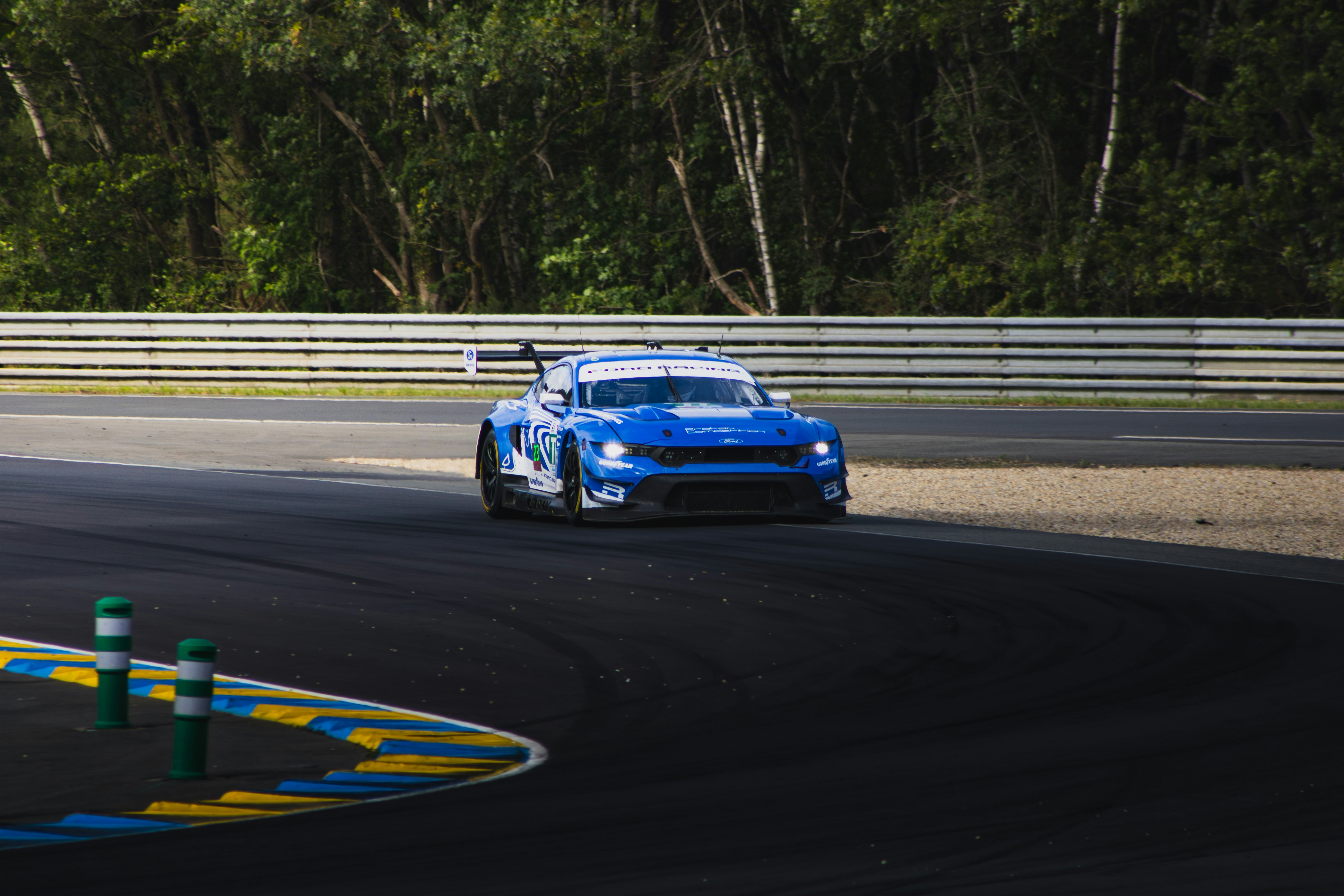 Blue race car rounds the bend under trees on a racing track