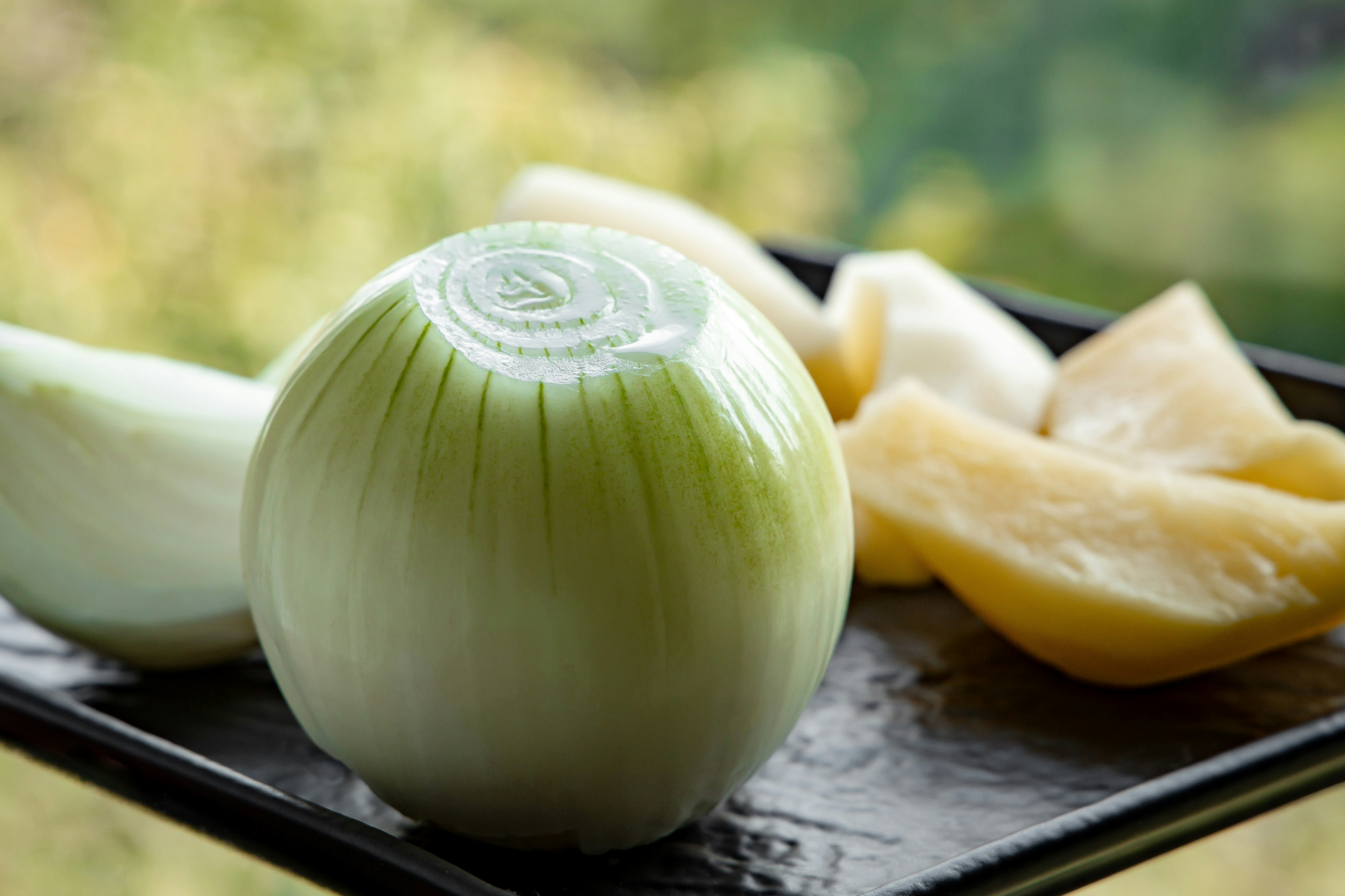 Green onion on a glossy black tray with pale potato wedges