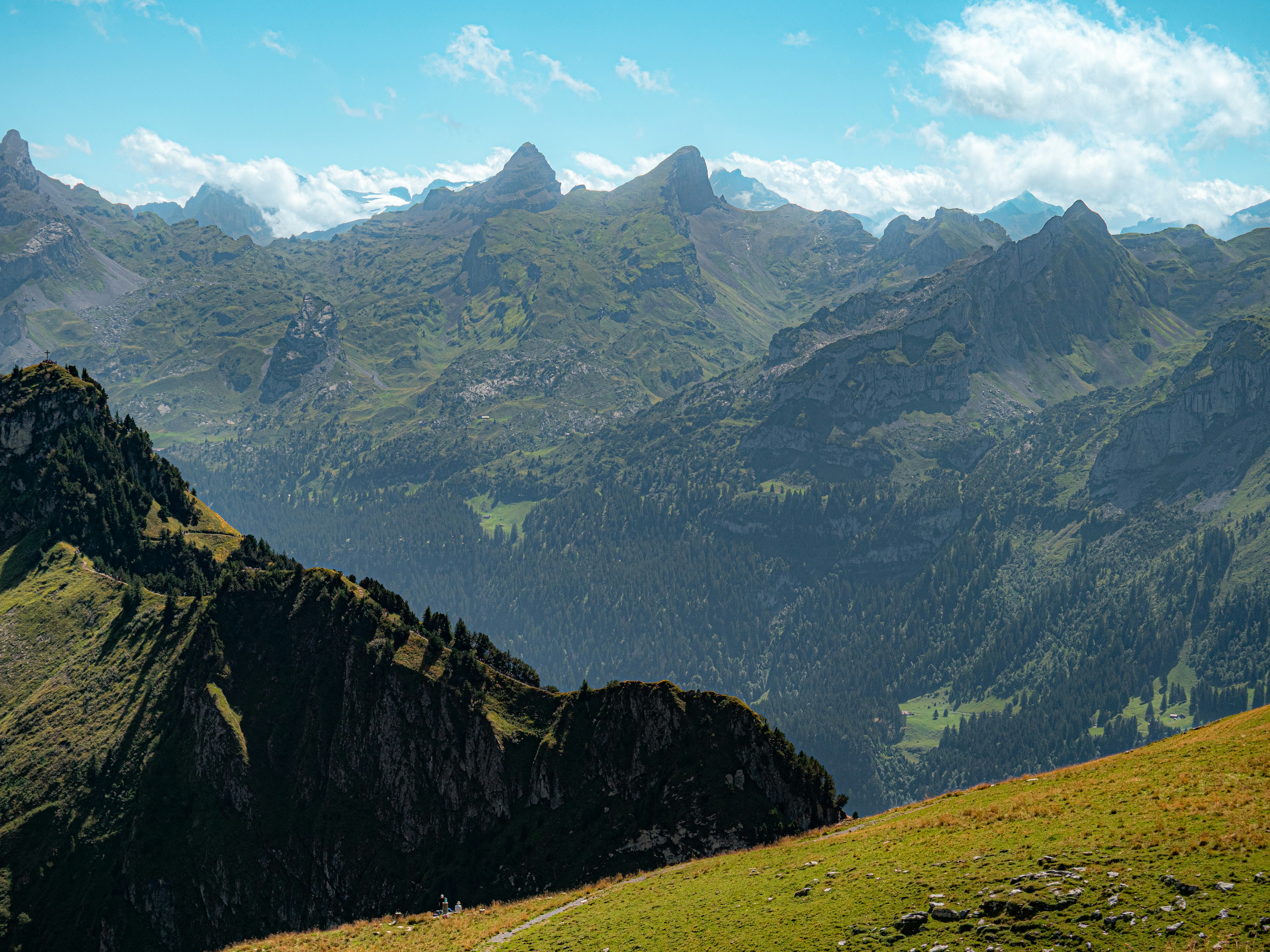 Ridgeline Echoes: Sunlit Peaks Over a Valley Carpeted in Green