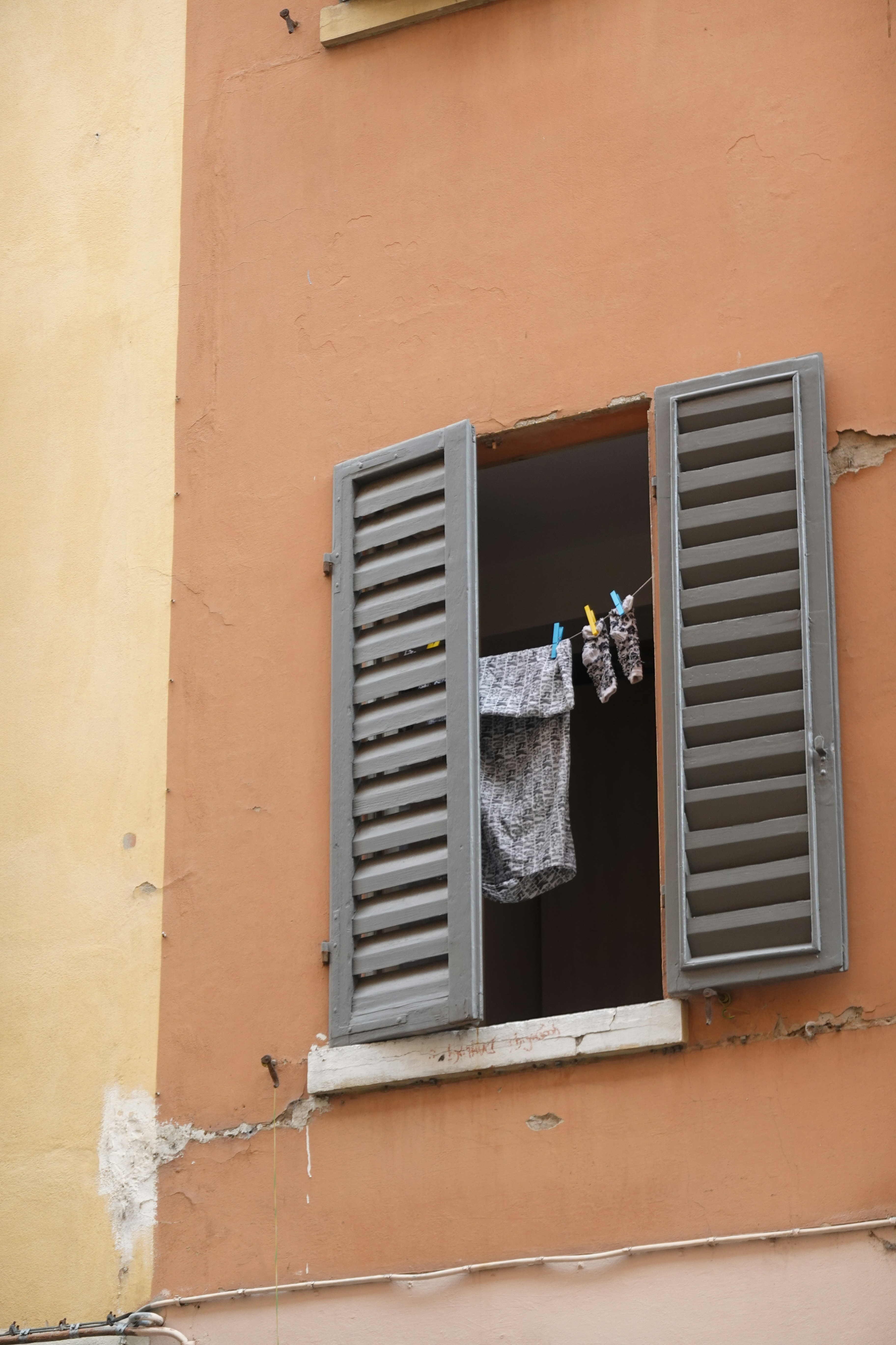 Laundry hanging on a line inside an open window with grey shutters
