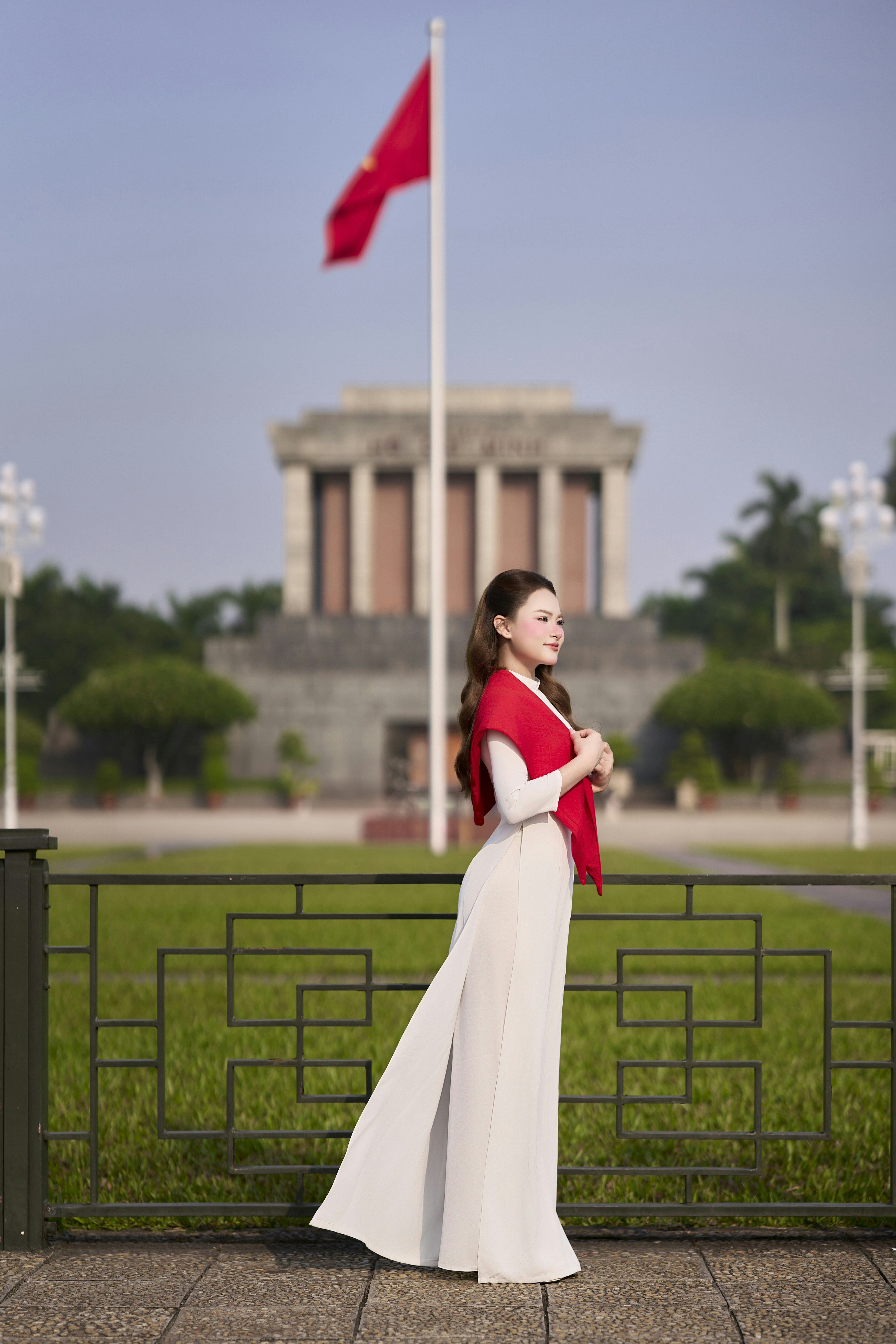 Red scarf, white gown: a portrait beneath the flag at the national plaza