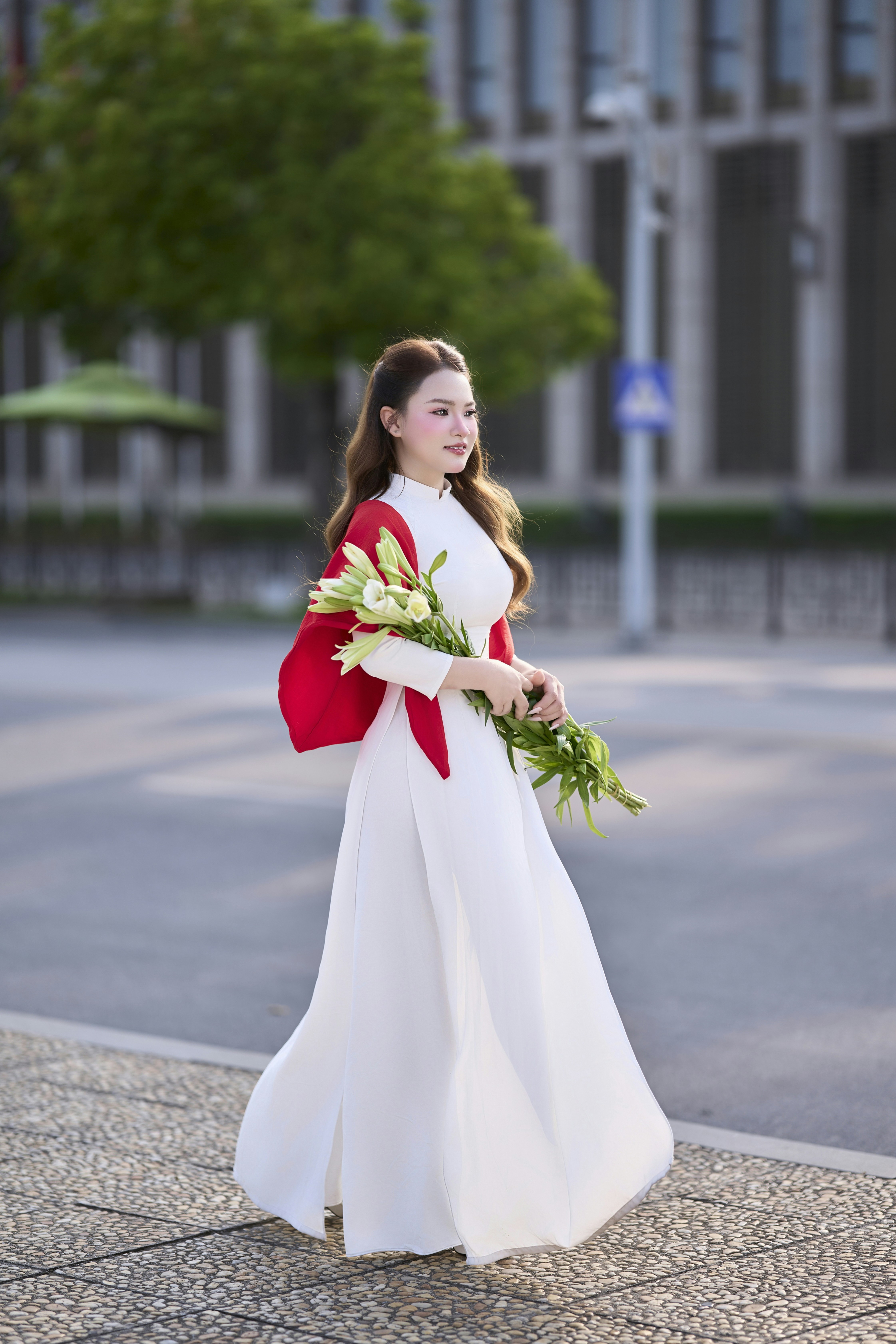 Portrait in White: A Bride-like Figure Walks with Lily Bouquet through an Urban Square