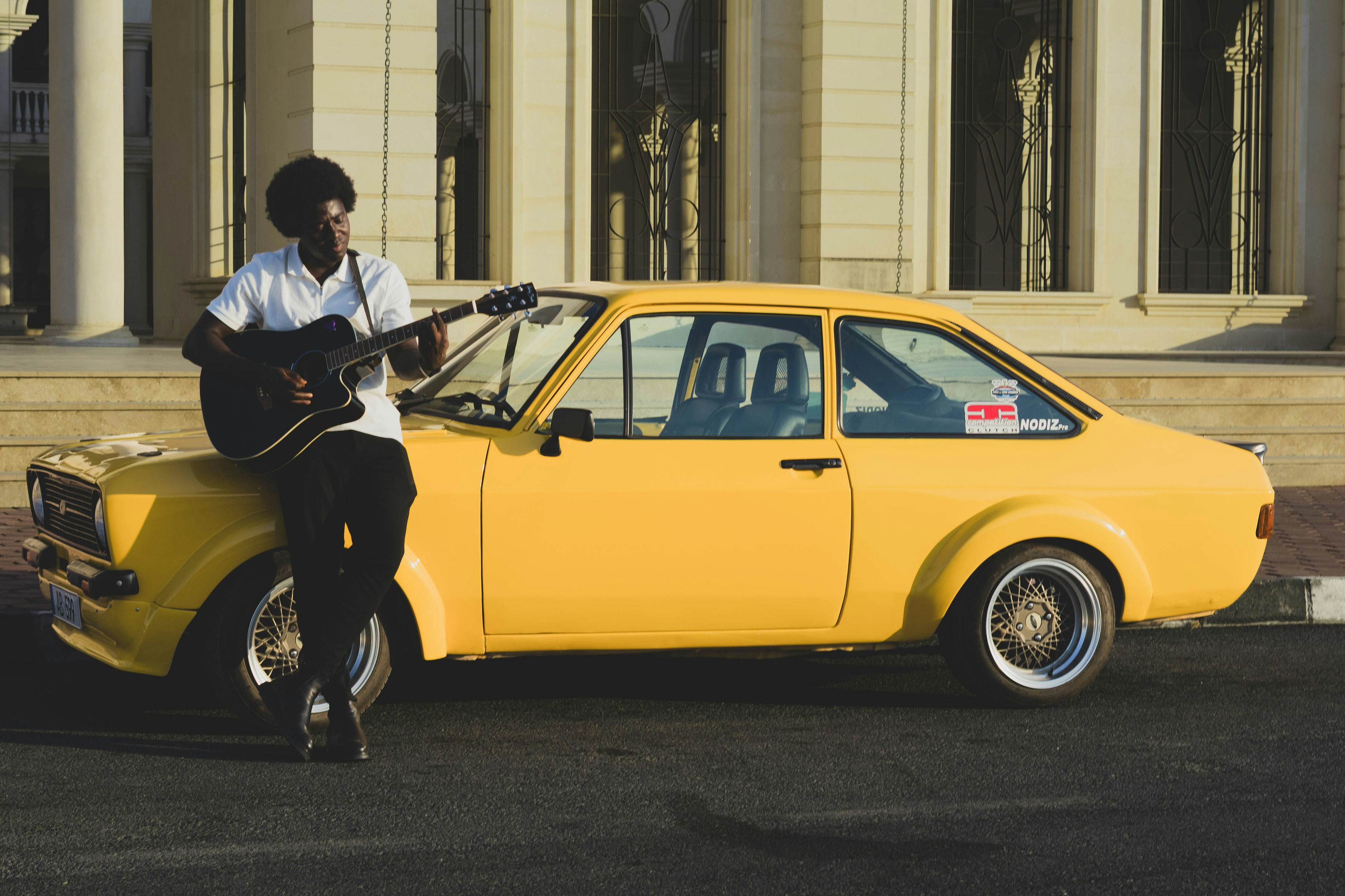 Yellow coupe Serenade: A guitarist in front of a vintage ride