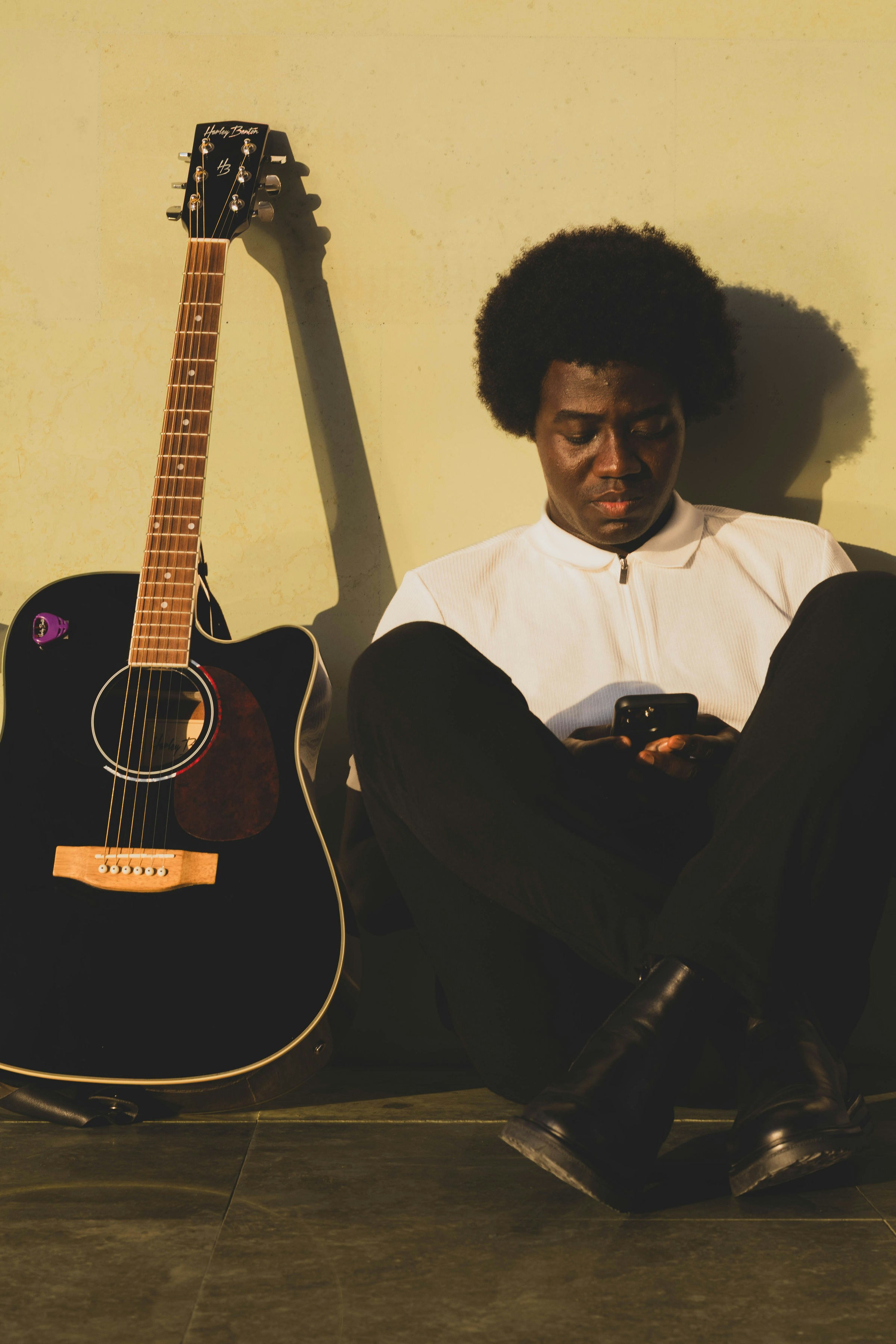 Quiet Pause: a guitarist rests with a phone against a sunlit wall
