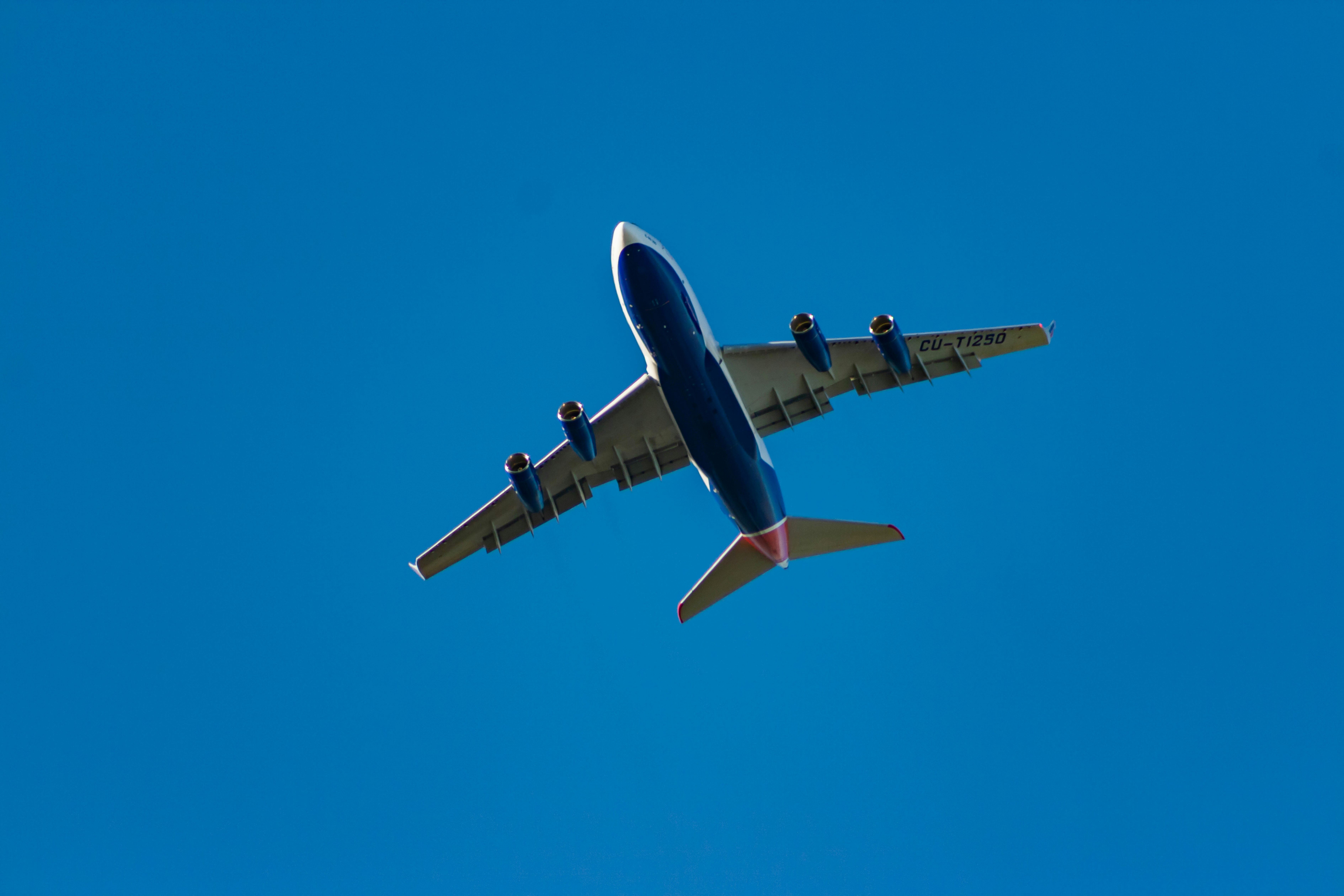 Sleek commercial jet photographed from below against a vivid blue sky, highlighting the aircraft’s underside and wing details.