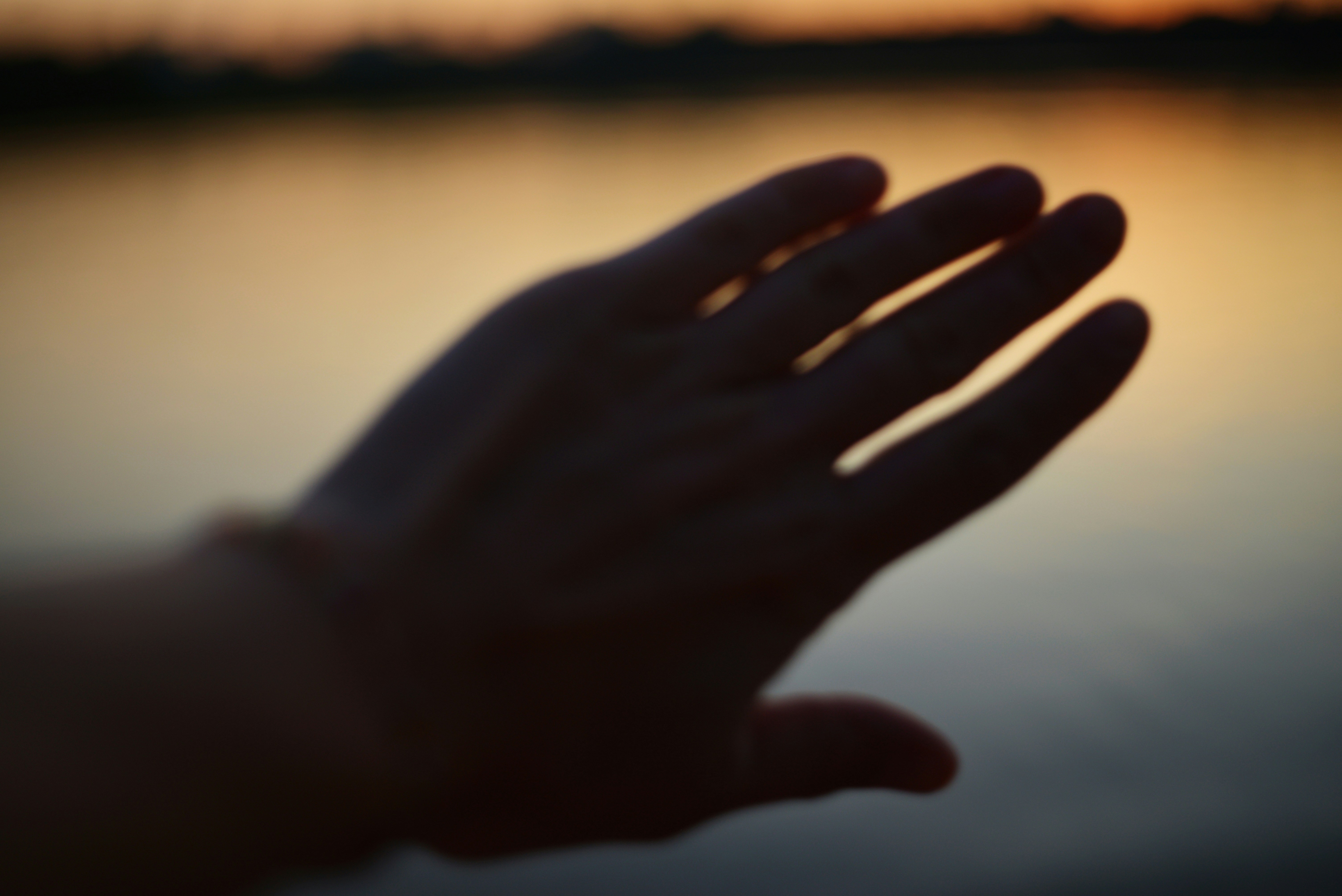 Silhouette of an Open Hand Against a Sunset Lagoon