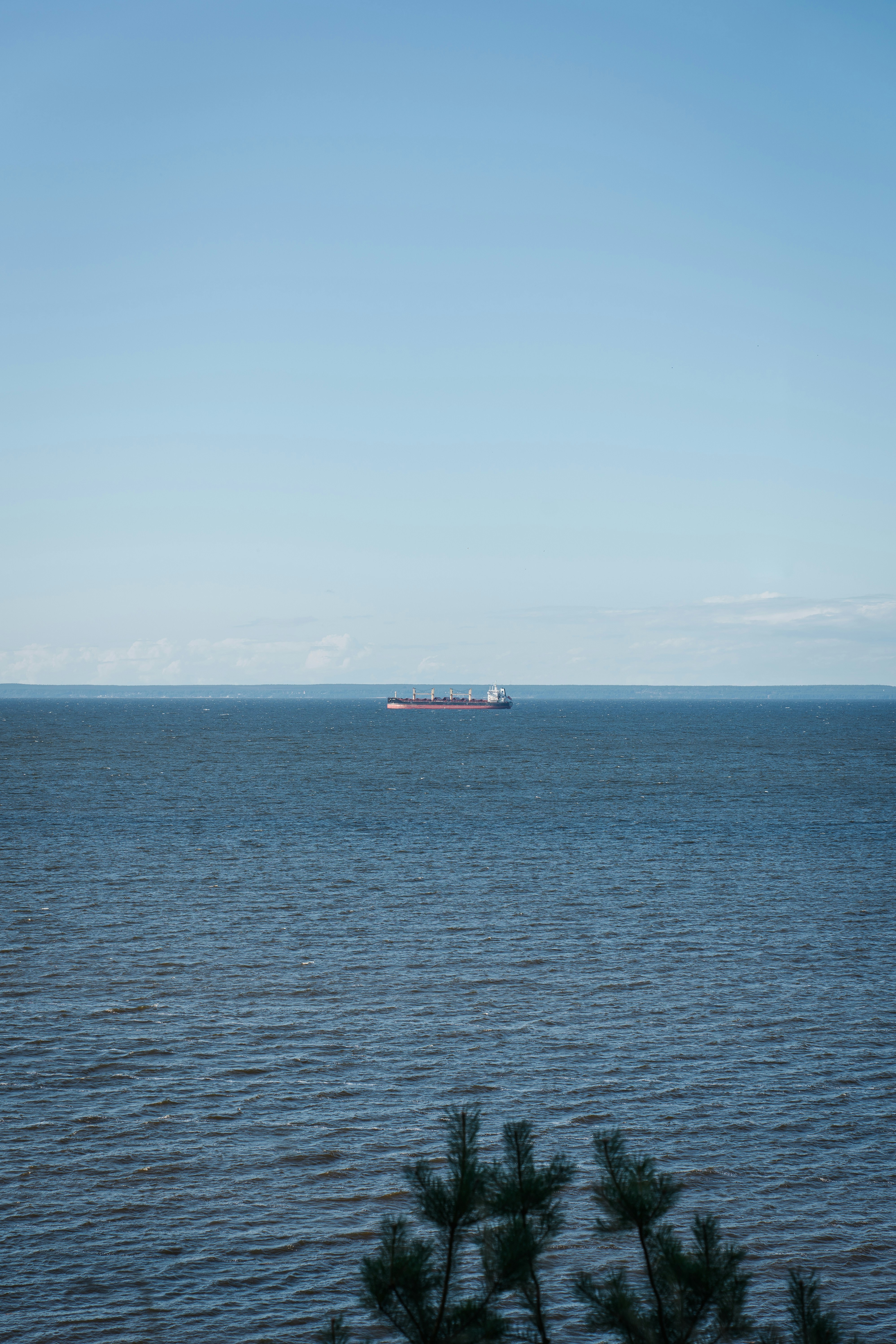 A lone cargo ship on a tranquil sea under a pale morning sky