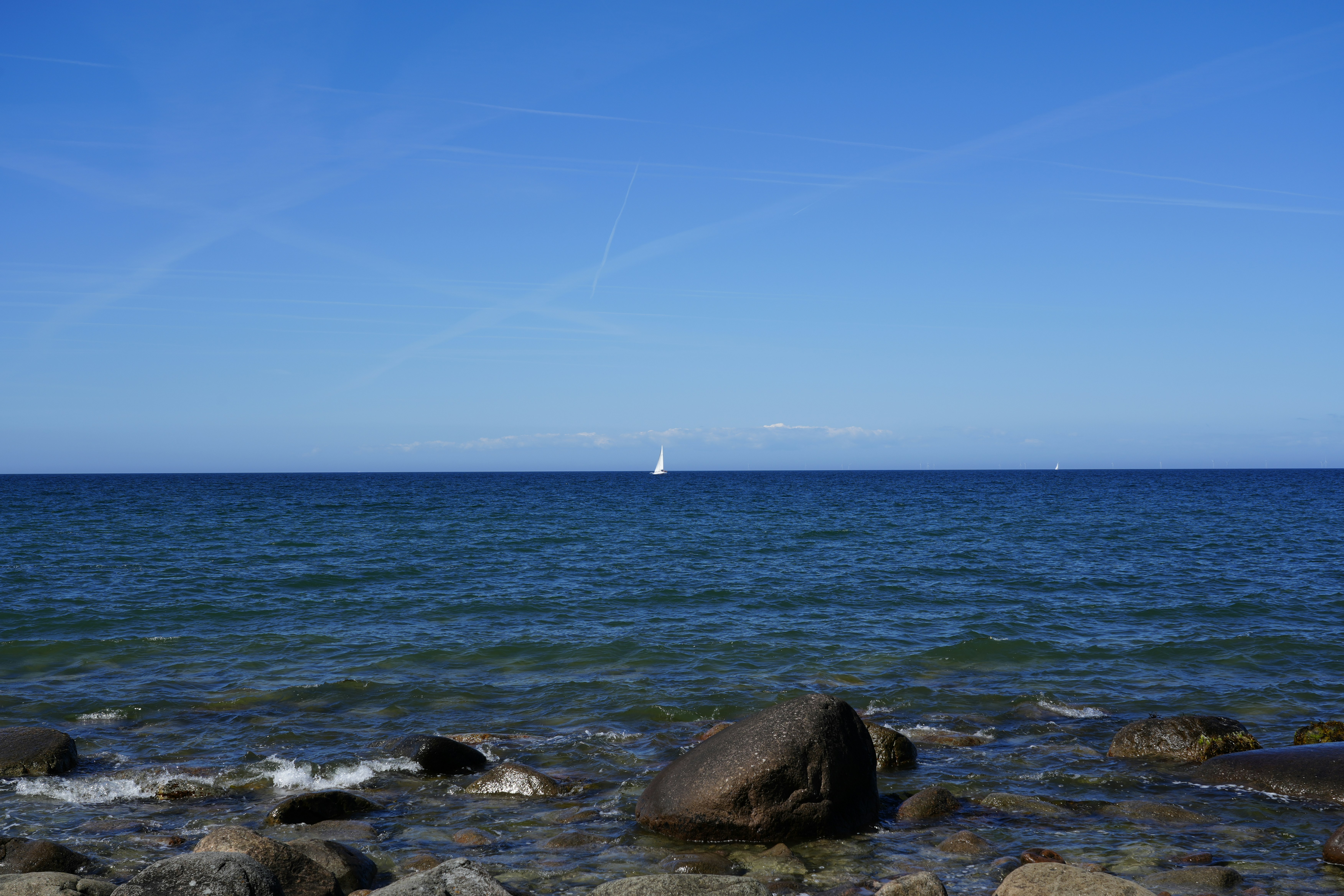 Horizon Sail: A lone white sail on a calm sea