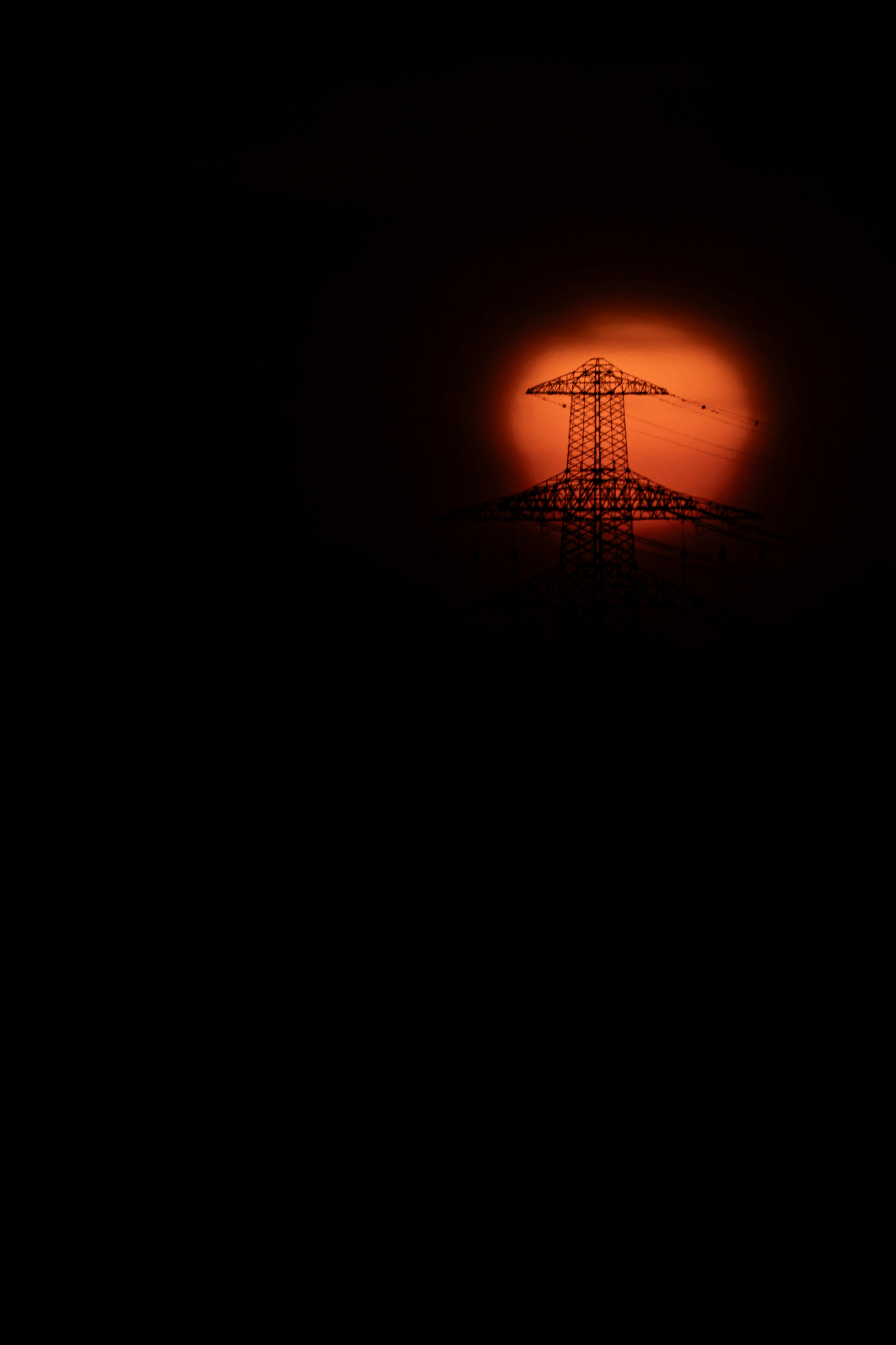 Sunlit silhouette: a towering lattice of power against a crimson horizon