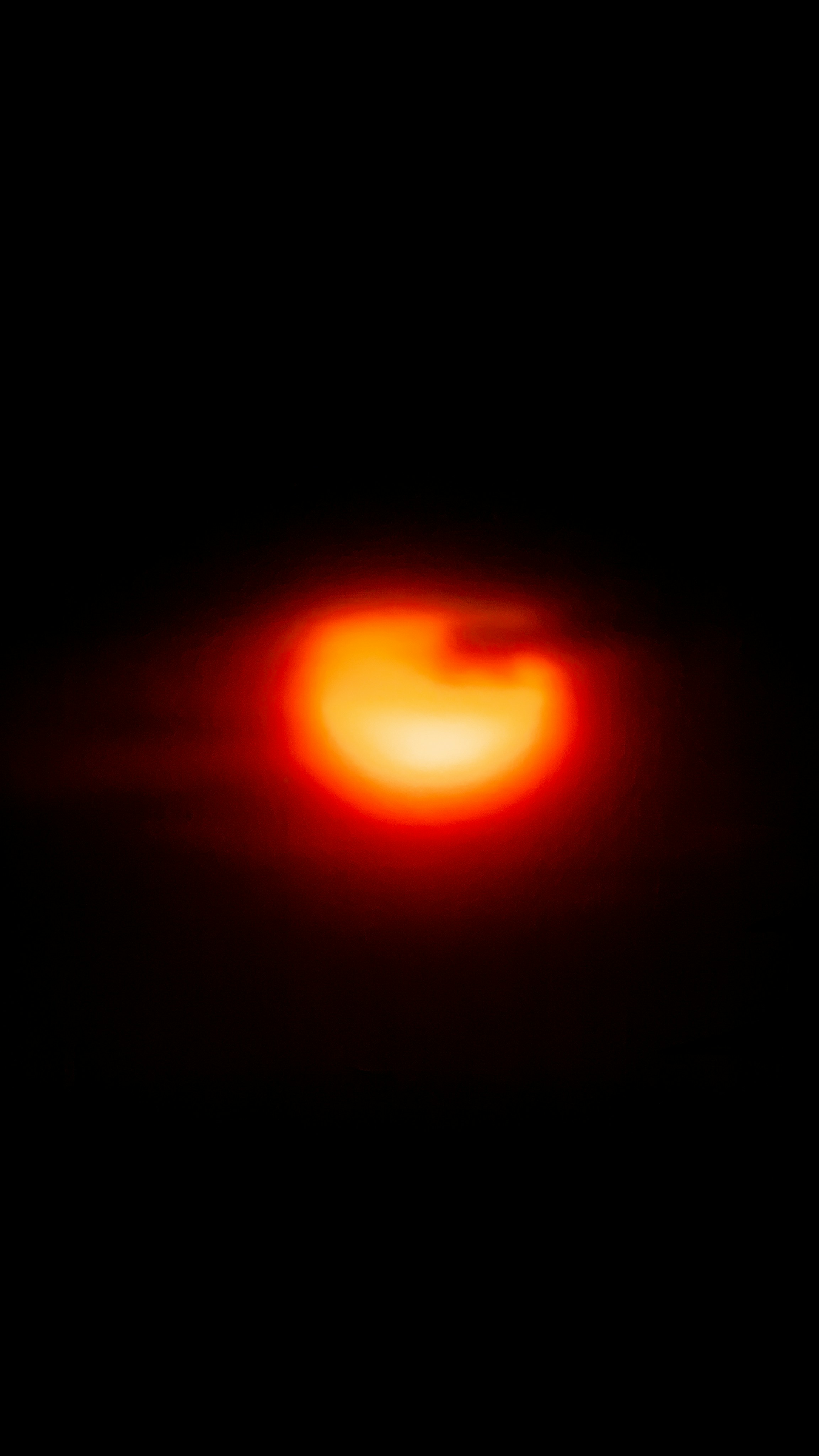 A glowing red orb against a black night; the image conveys a distant, out-of-focus light source with soft haze around it. This is a photographic capture rather than a painting or illustration.