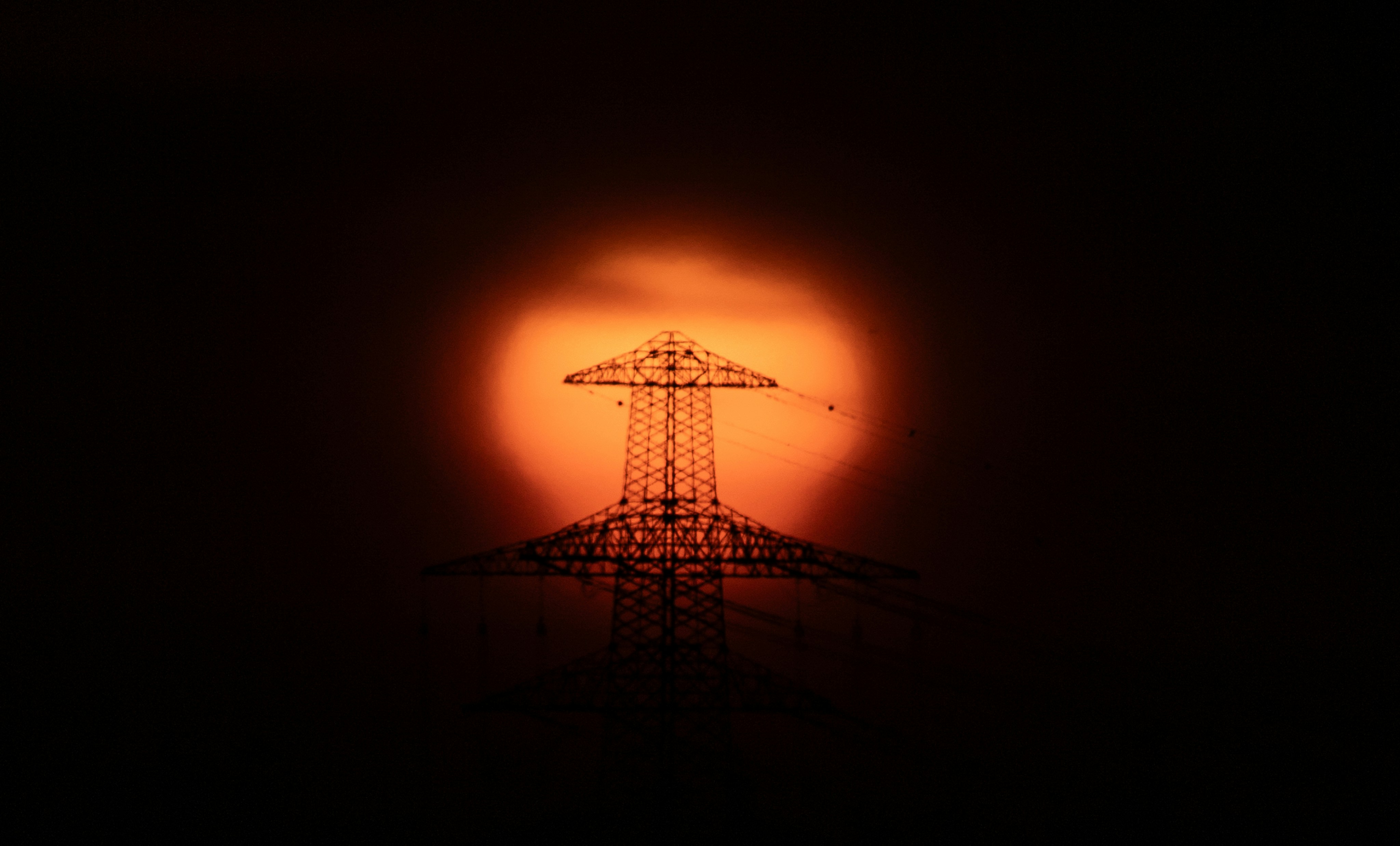 Sunset silhouette: power lines cradled by a molten orb