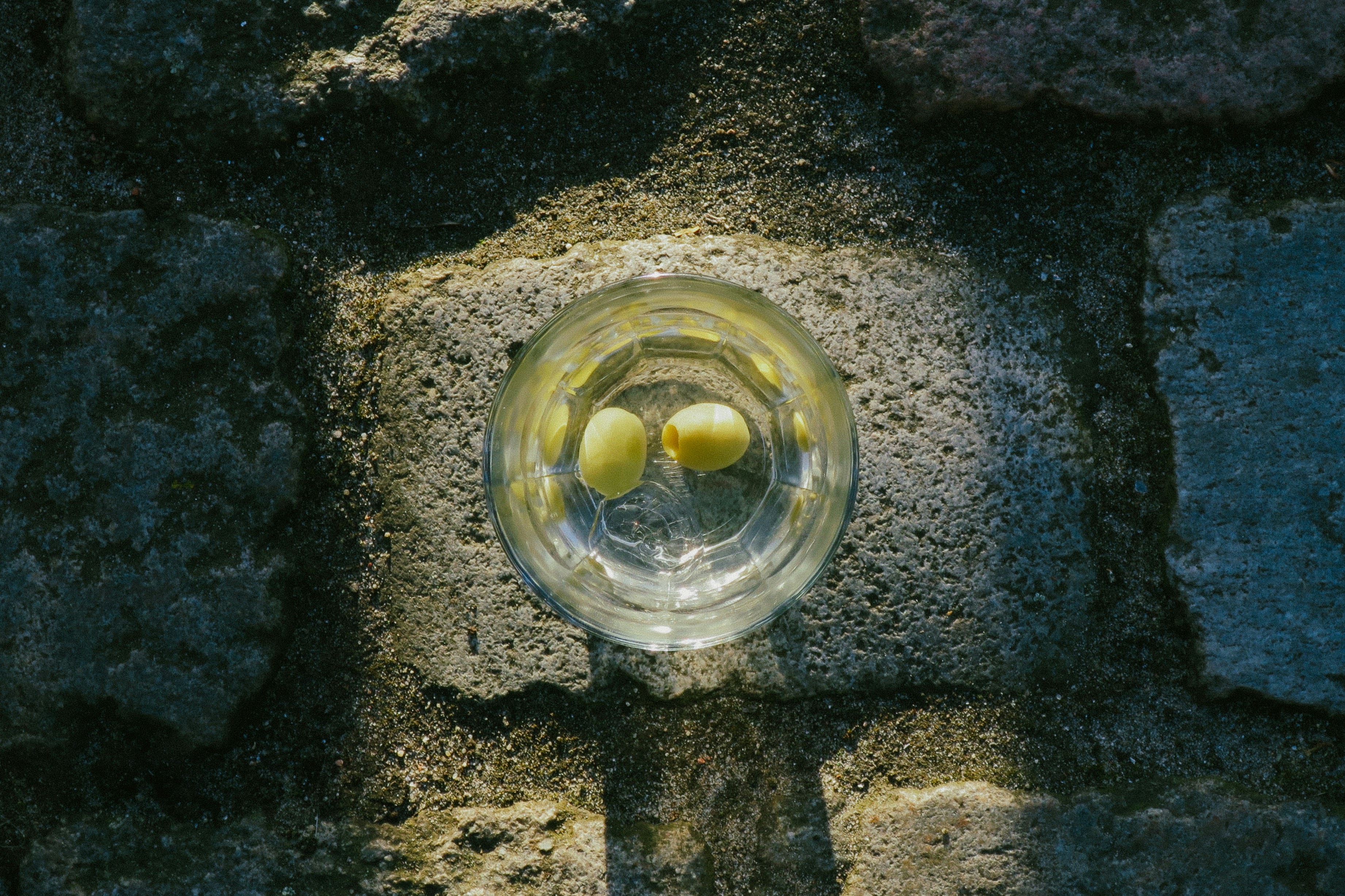 Circular glass lamp embedded in rough stone surface, catching a soft highlight and casting a gentle glow on textured masonry.