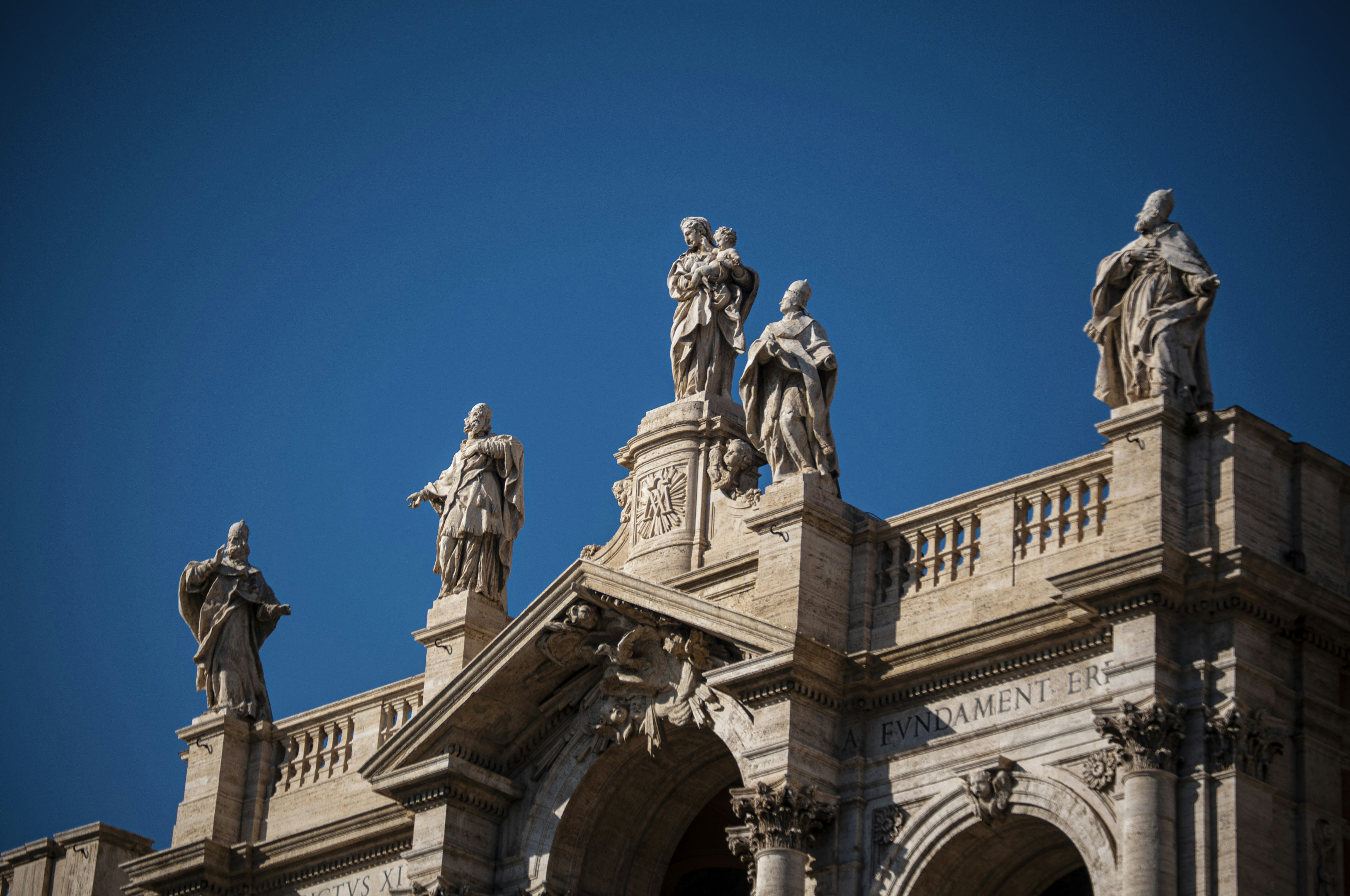 Stone Sentinels Crown the Arch: A Fragile Blue Sky Over Classical Facade