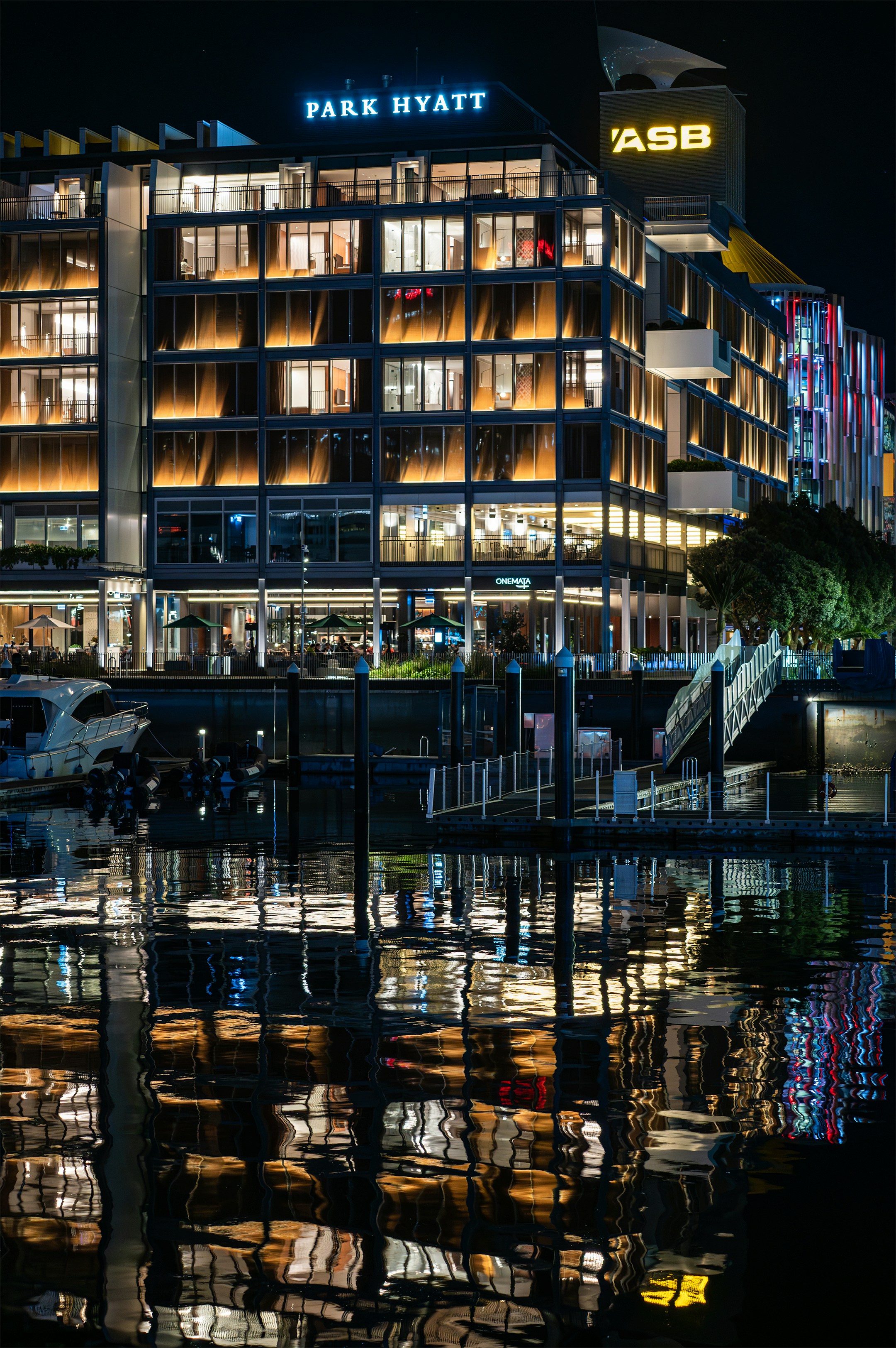 Nighttime view of a modern waterfront hotel with illuminated windows, reflecting on the rippled canal water.