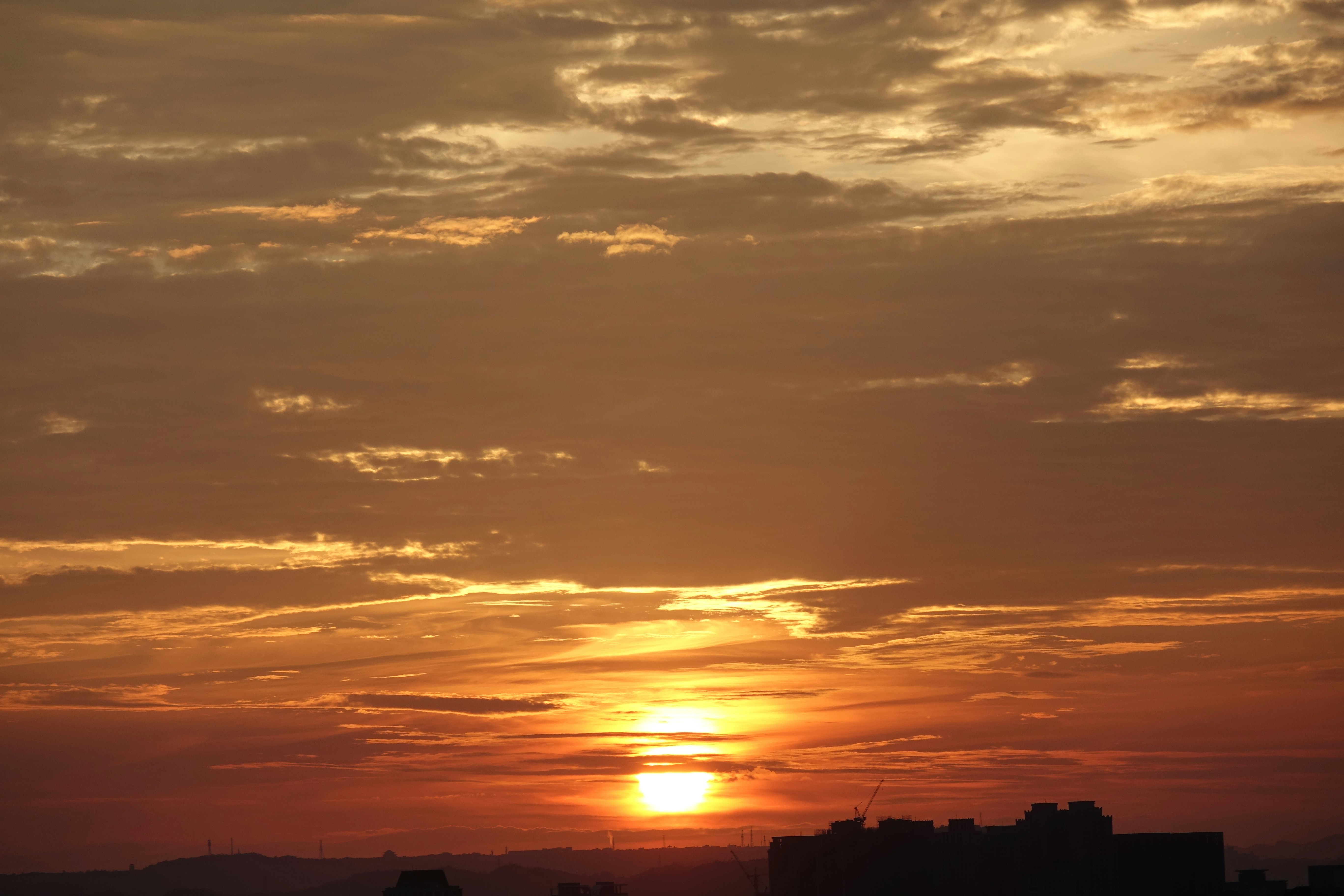Low sun glowing behind dark clouds above a silhouetted city skyline