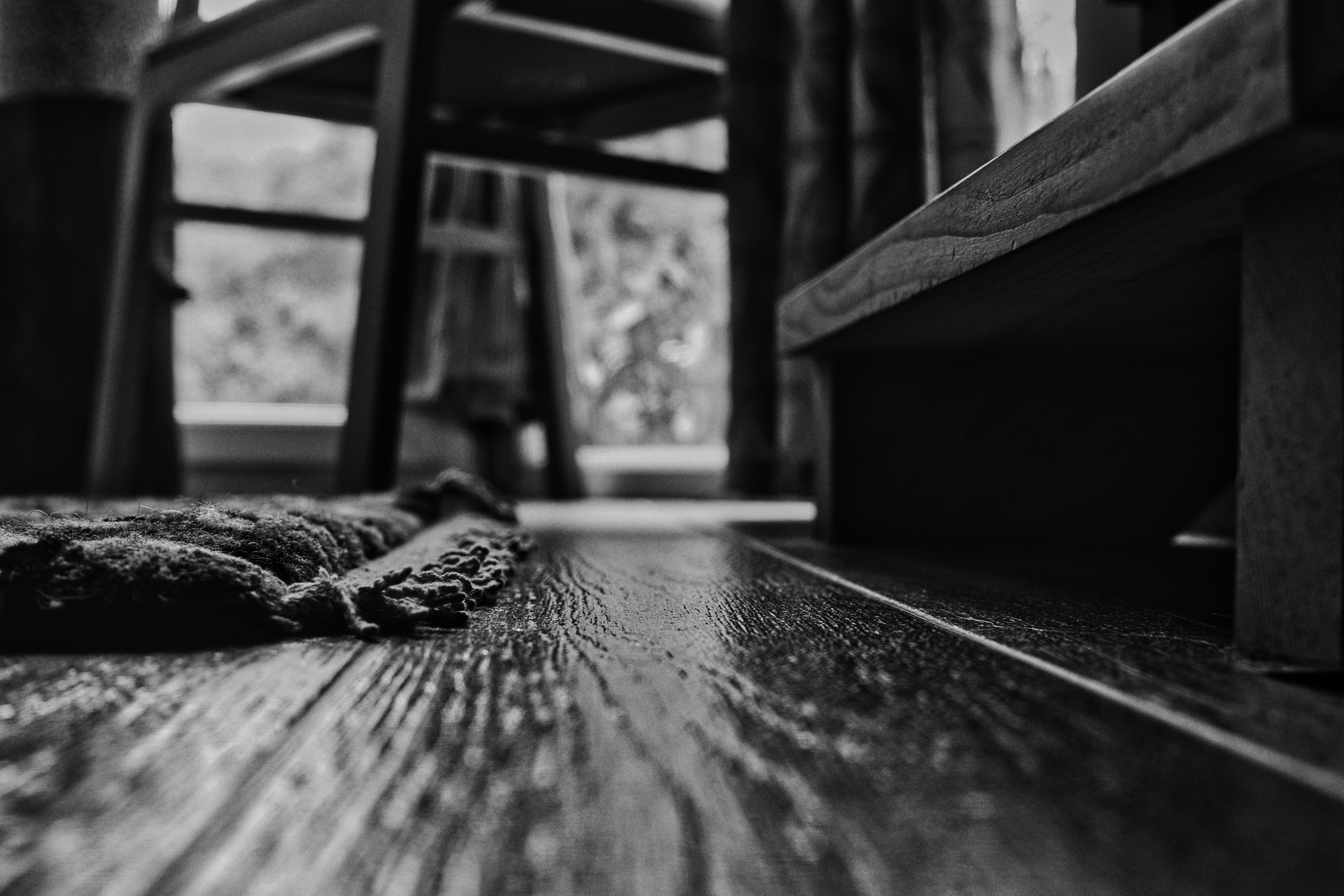 Low-angle shot of a wooden floor with a rug and furniture casting silhouettes; the scene emphasizes texture and depth with a shallow perspective.