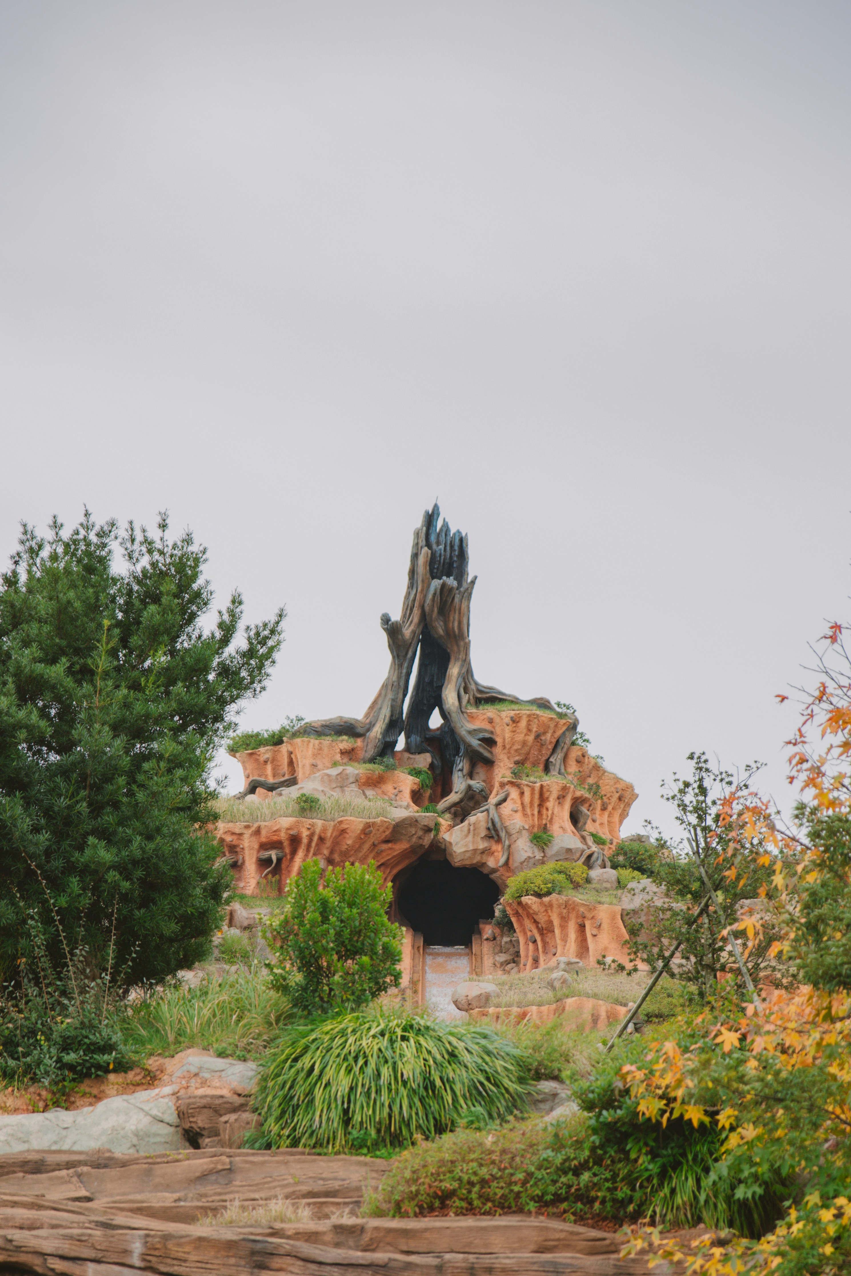 A large artificial rock formation with a dark tunnel entrance and a dead tree