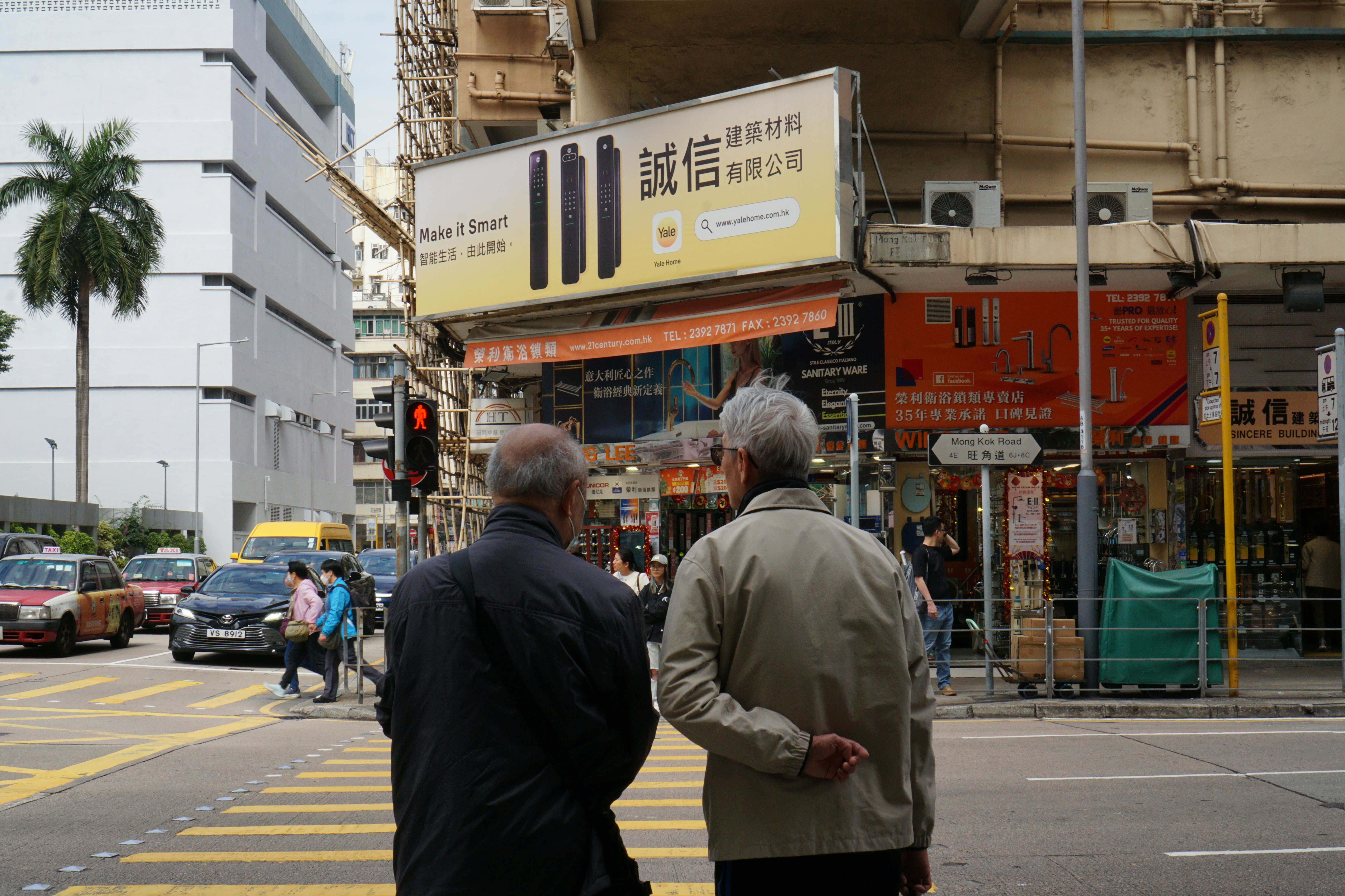 Two elderly men in a busy urban intersection gaze toward a storefront under construction