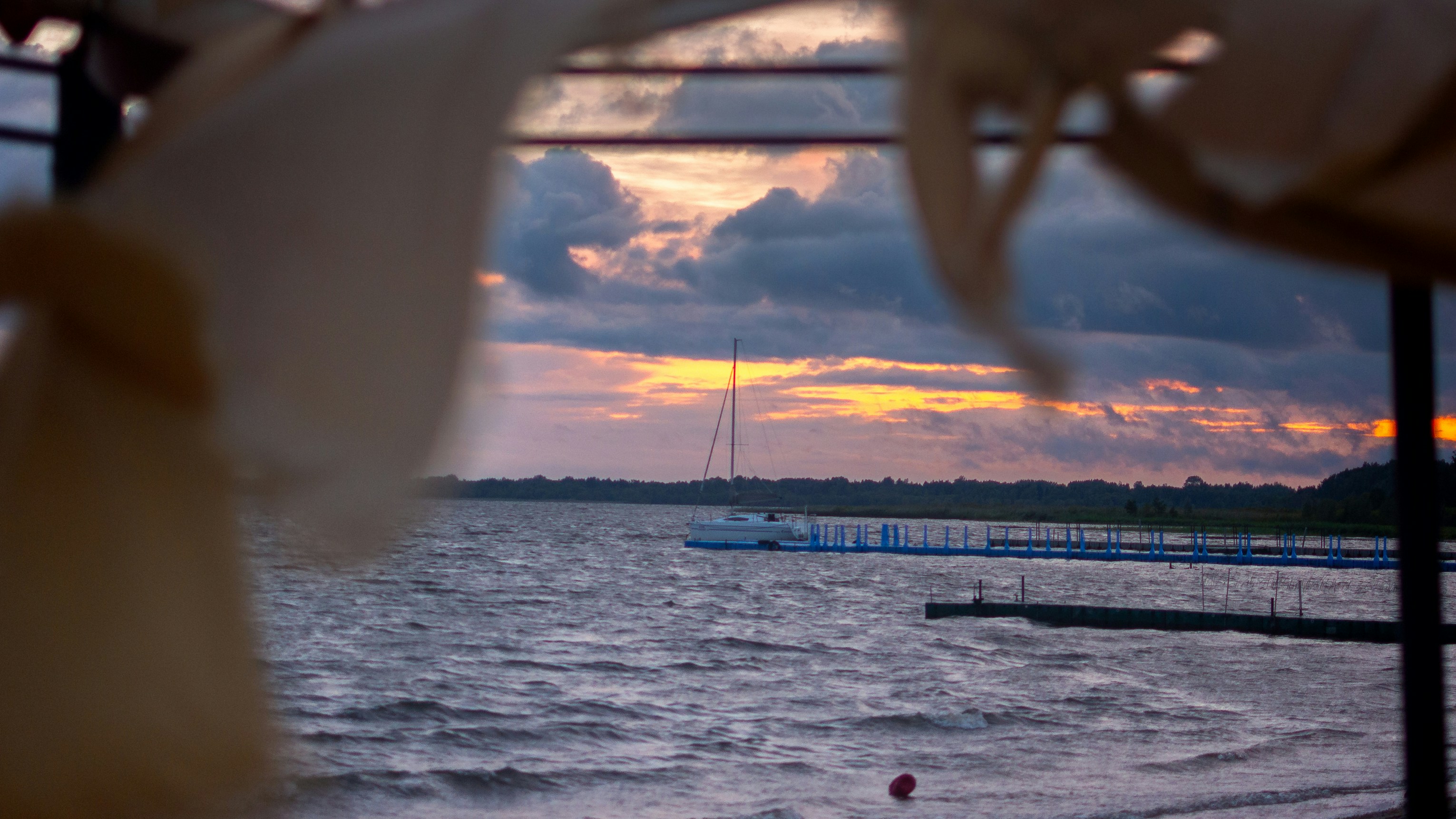 Sunset Over a Quiet Lake Framed by Distant Pier and Overhanging Leaves