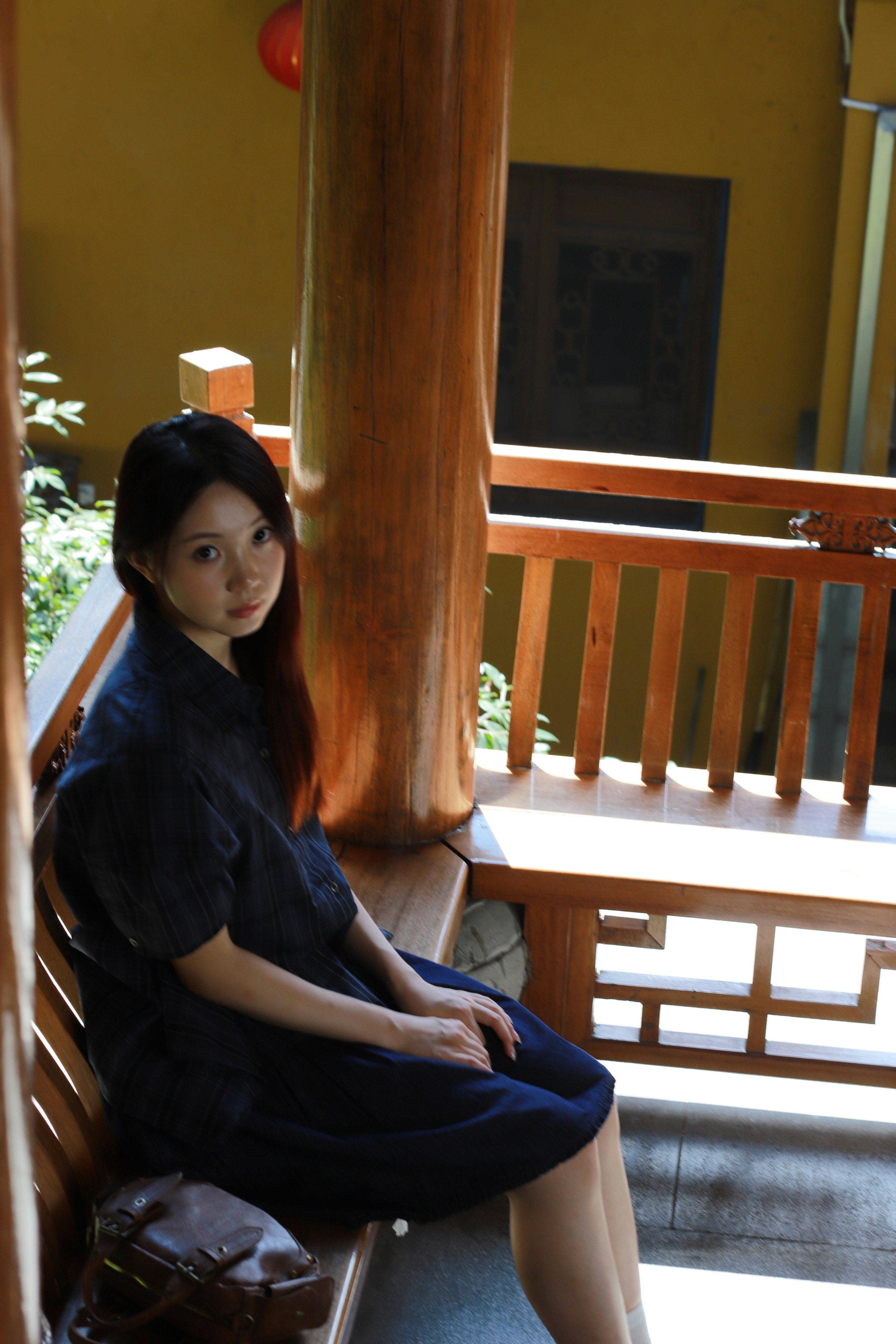 Woman in a navy dress resting by a wooden railing under a painted column