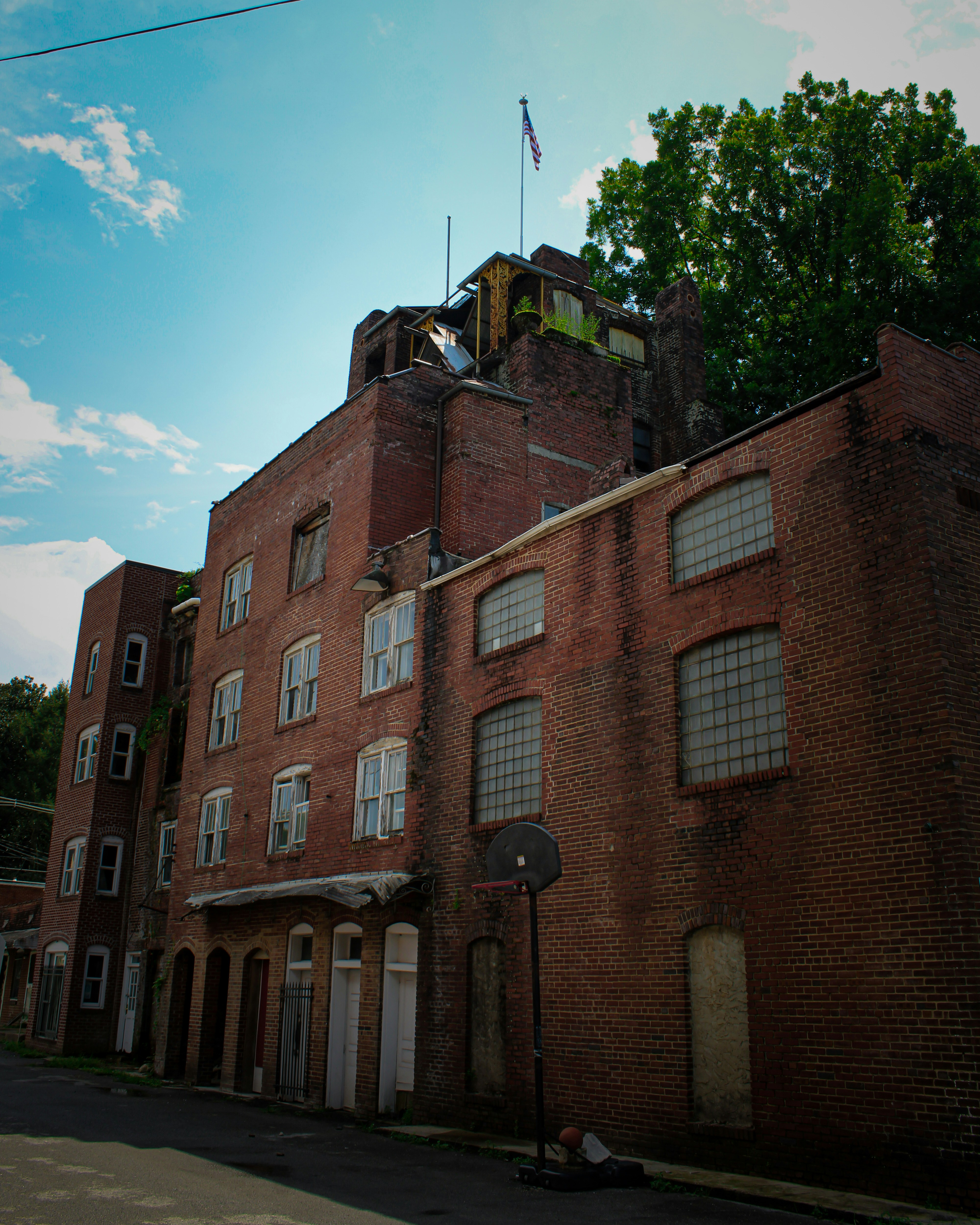 A weathered red brick building with many windows and a basketball hoop outside