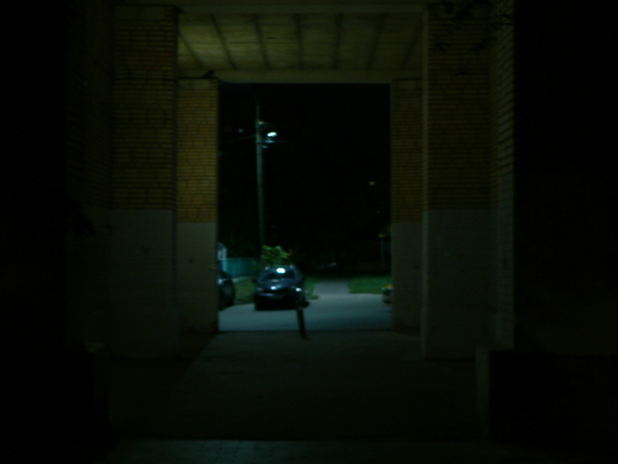 Night Corridor: A Lone Car Emerges Beyond the Pillars