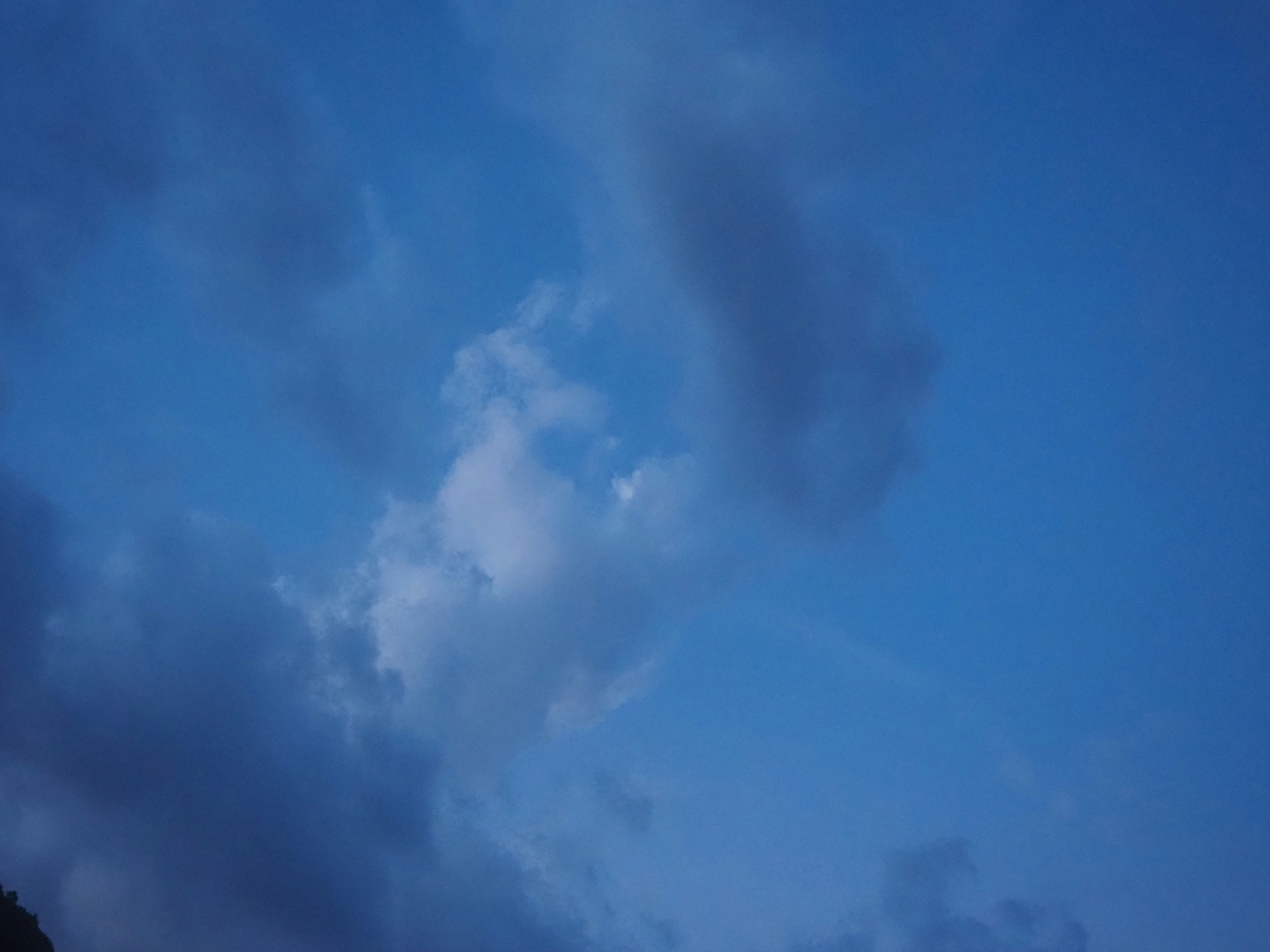 Bright blue sky with scattered clouds occupying the upper two-thirds of the frame; minimal land appears along the lower left edge, conveying a calm, expansive atmosphere.