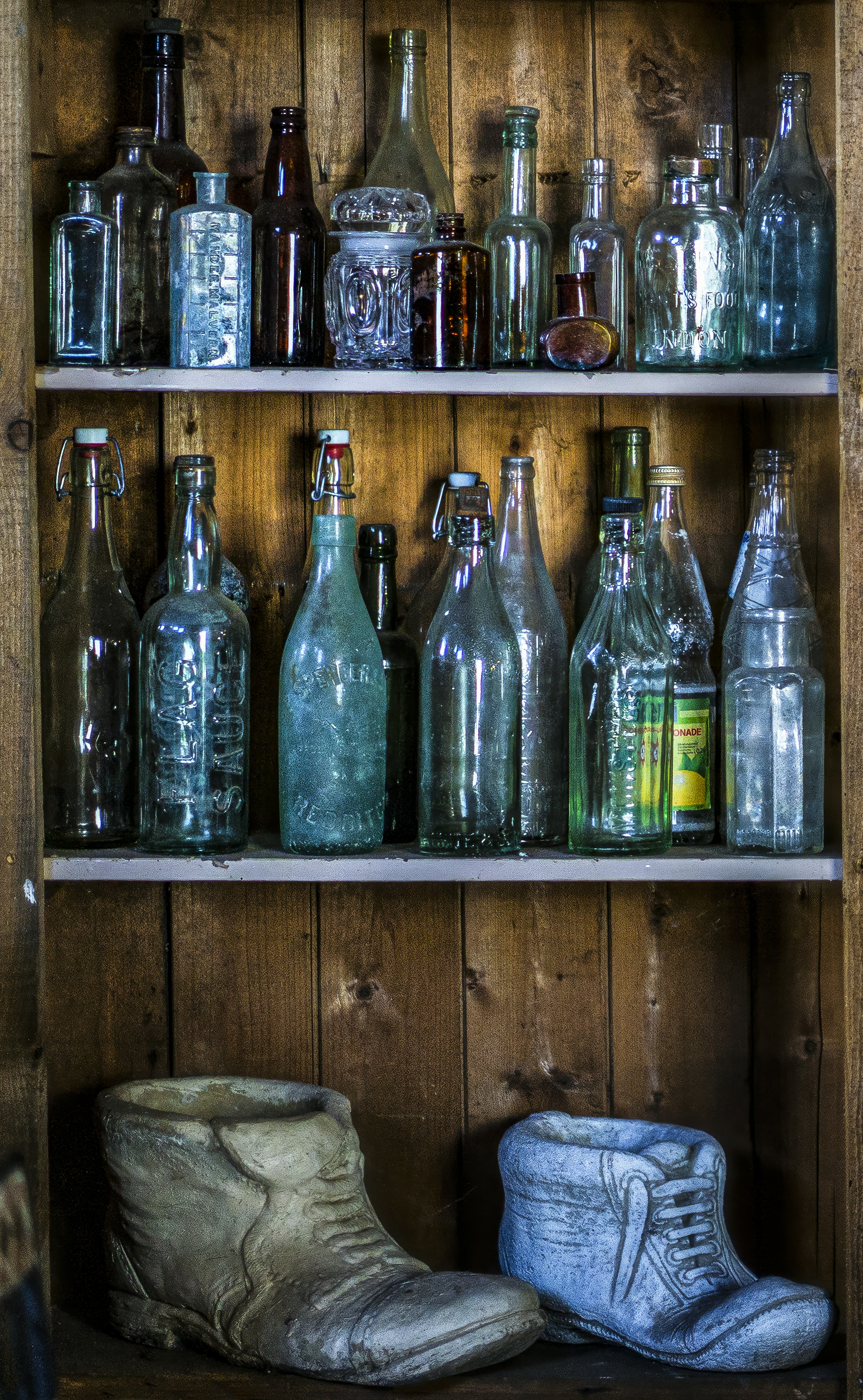 Blue Glass on Wood: A Rustic Shelf of Bottles Above Weathered Boots
