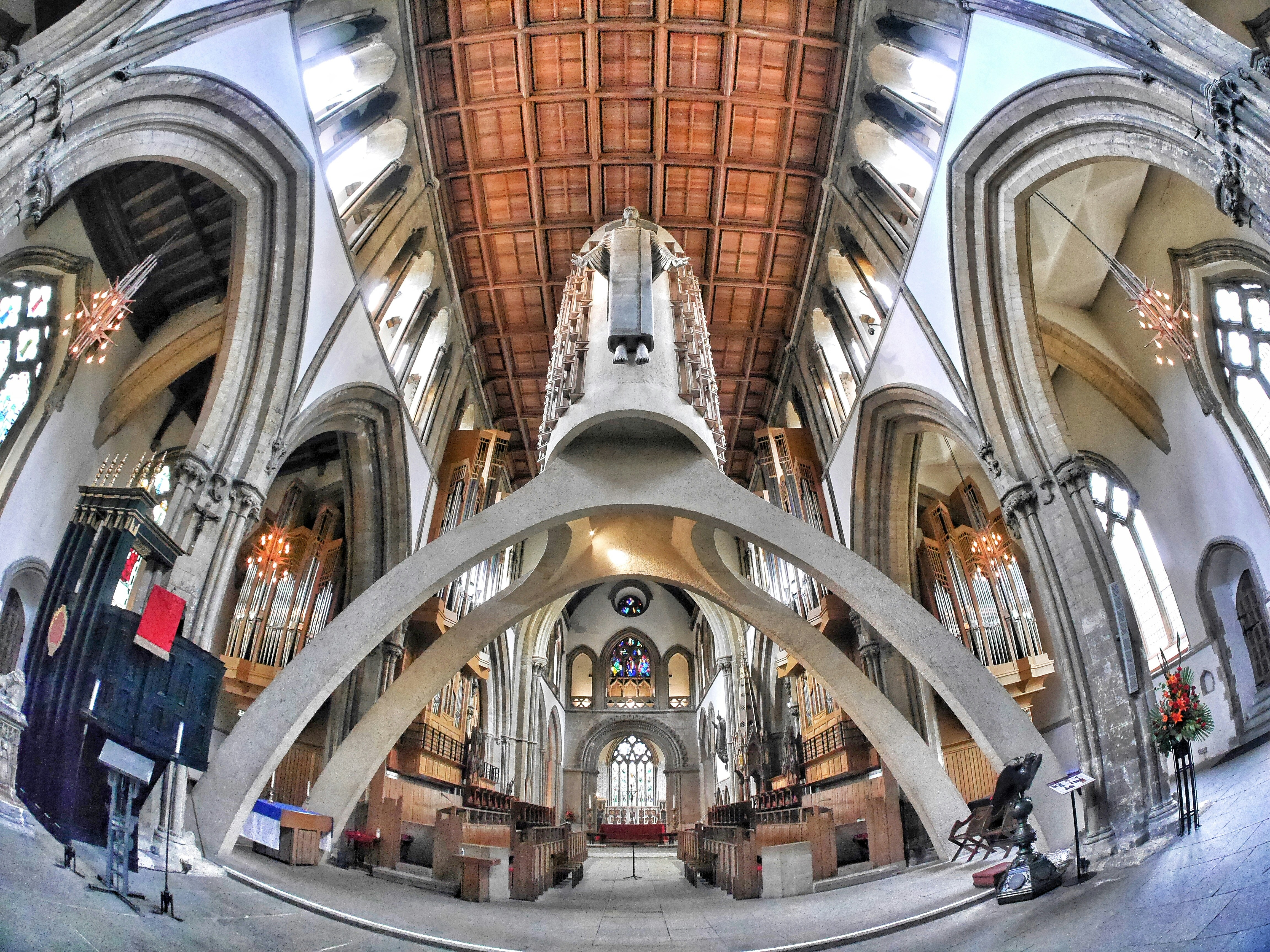 Interior of a grand church with a central sculptural arch and soaring vaulted ceiling, pews on either side, and stained glass at the far end; a wide-angle view emphasizing symmetry and scale.