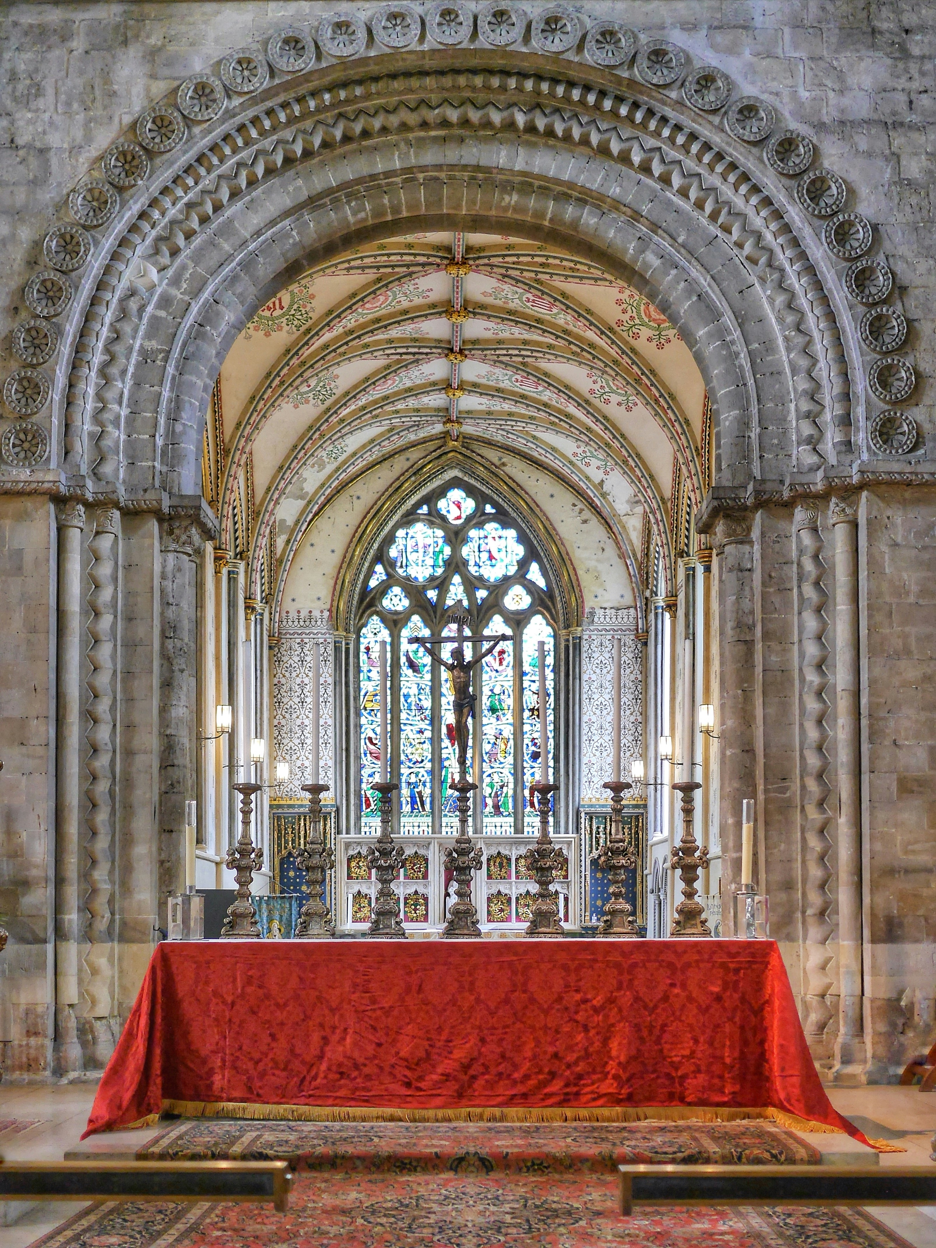 Red altar cloth with ornate chapel backdrop and stained glass windows inside a stone church.