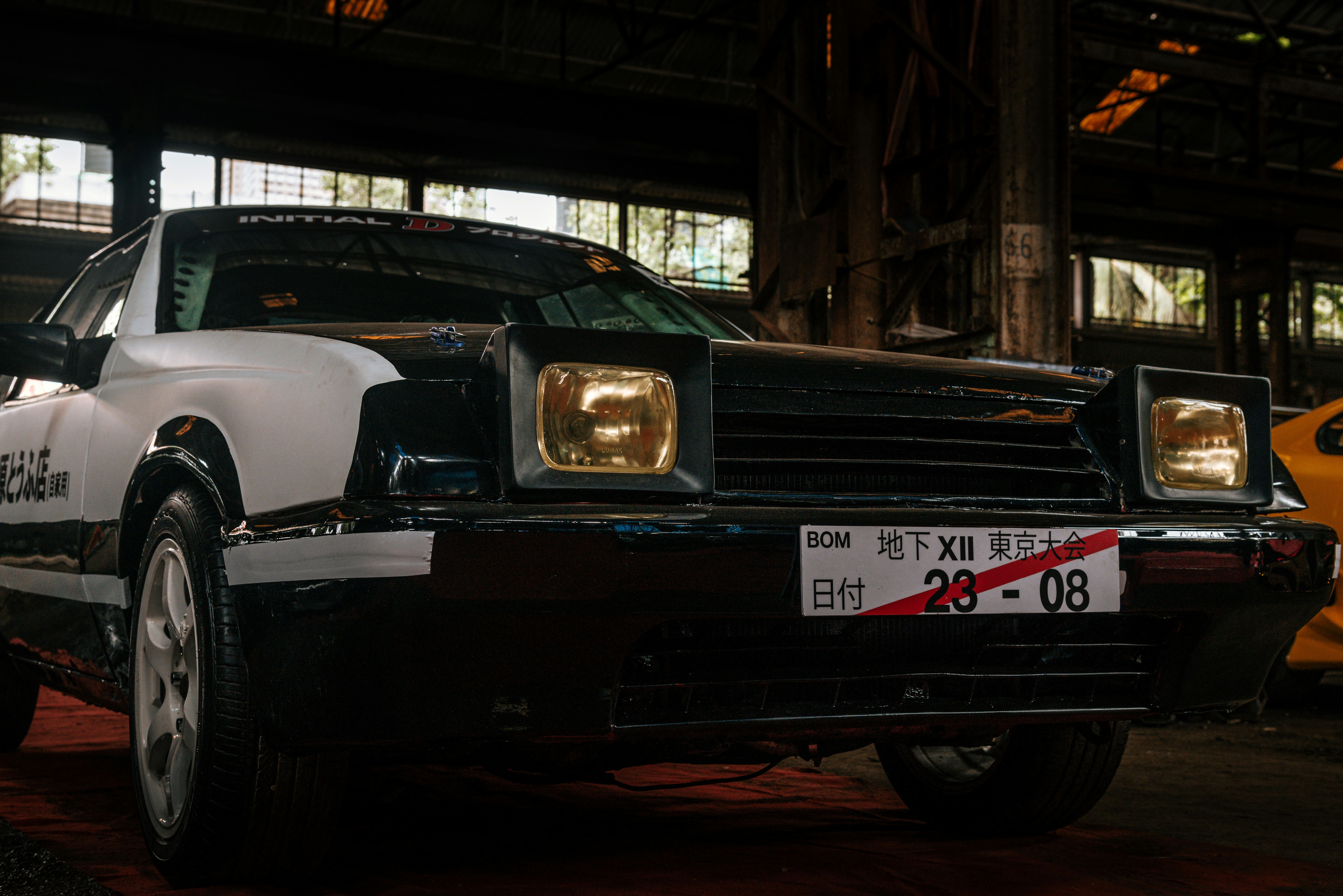 Shadowed vintage taxi in an industrial setting, front-end details and license plate catching dim light.